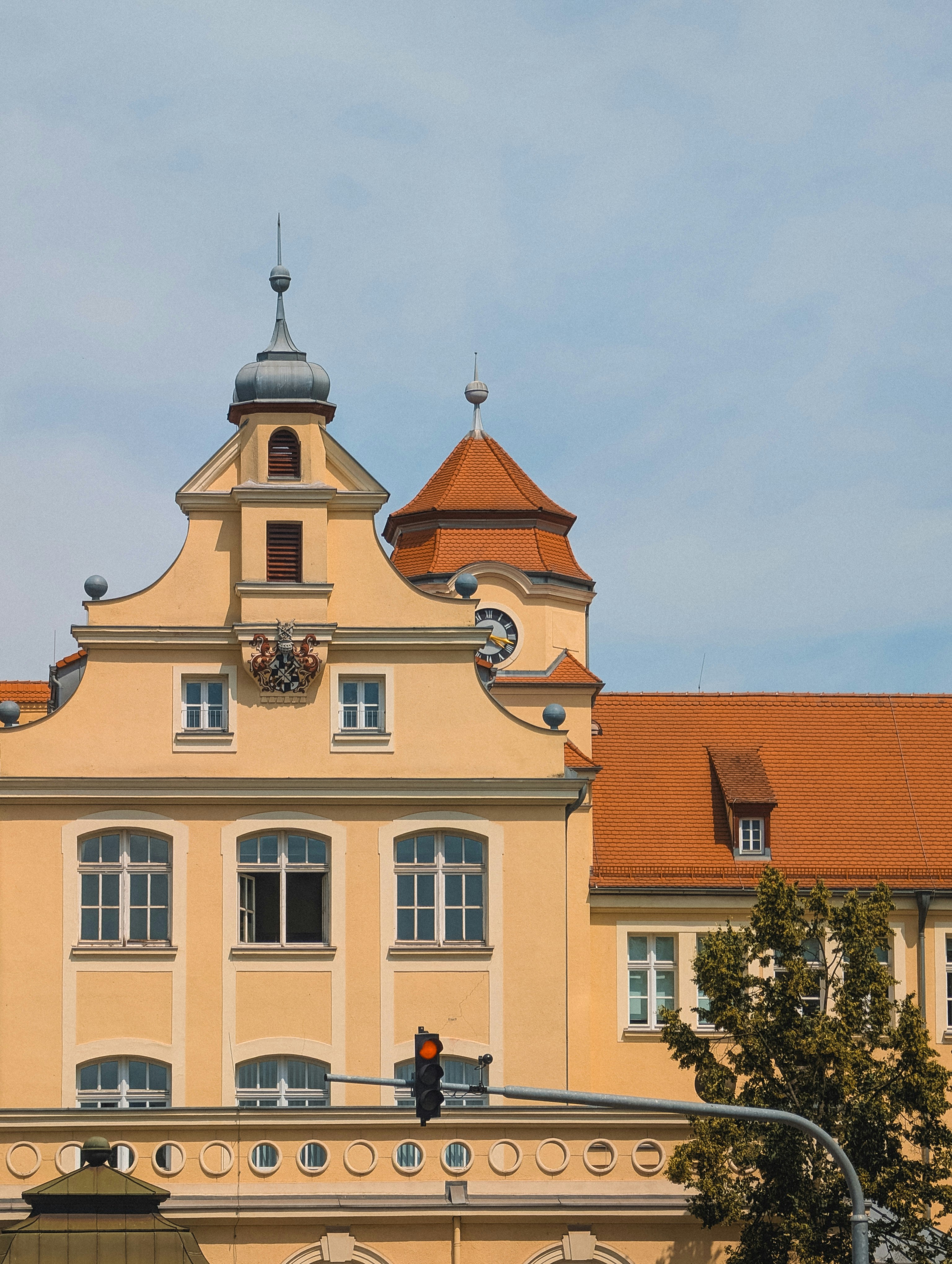 Historic building with intricate architectural details, featuring a prominent clock tower and vibrant yellow facade. Traffic light in foreground adds a modern contrast.