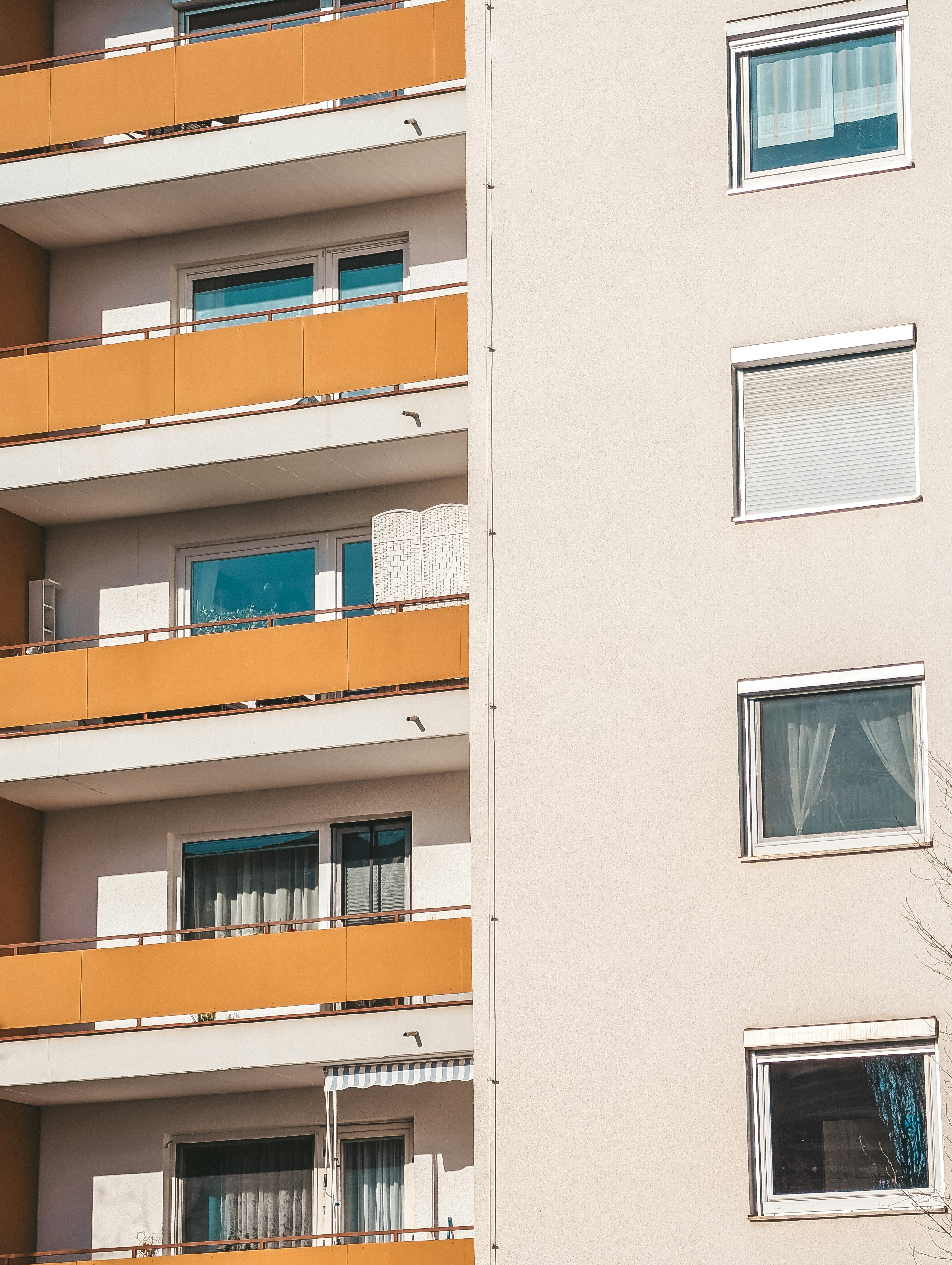 Balconies of a modern apartment building feature vibrant orange railings and varied window treatments, showcasing urban living aesthetics.