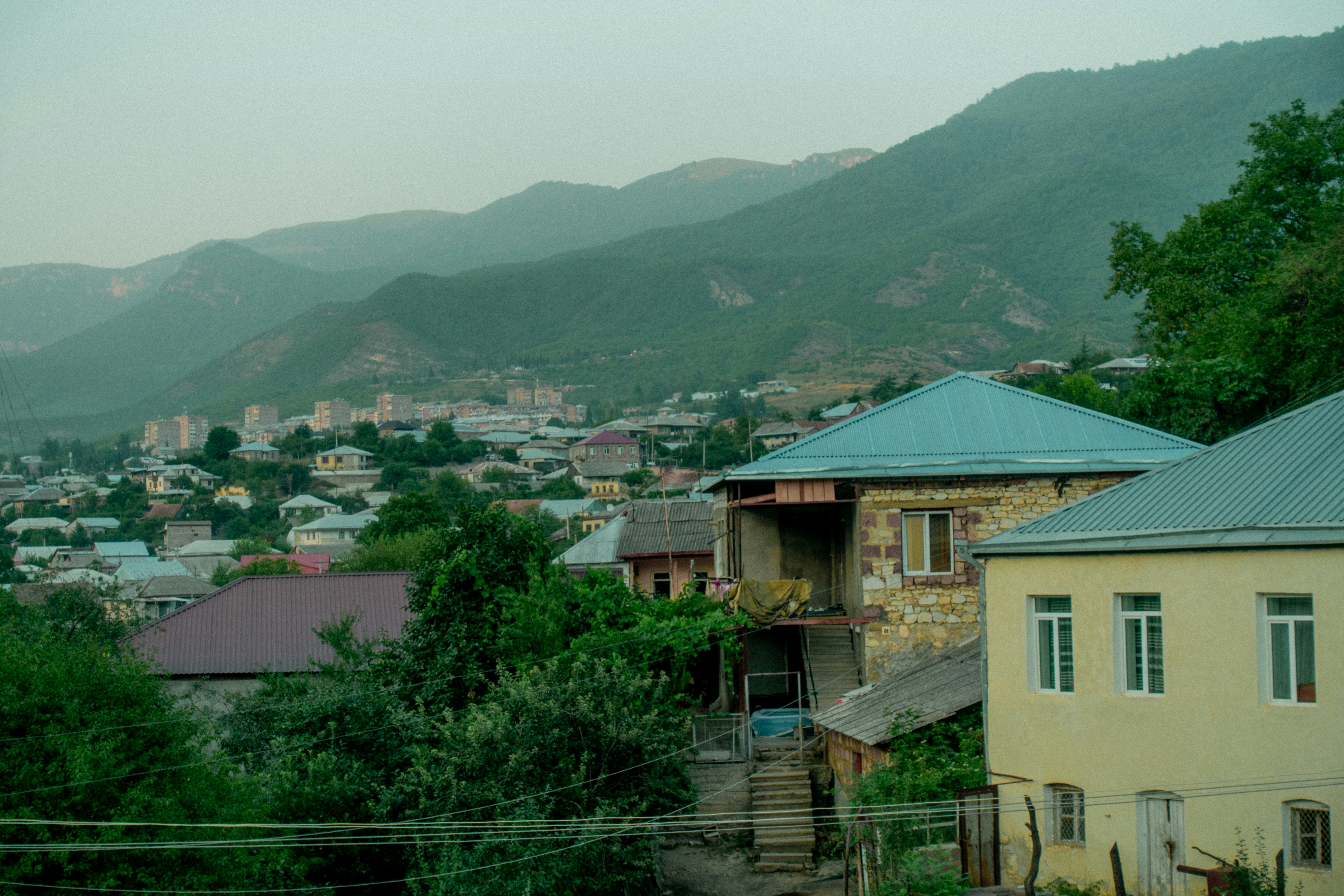 A serene view of a hillside town nestled among mountains, showcasing a mix of traditional and modern architecture. The scene captures the tranquil essence of rural life.