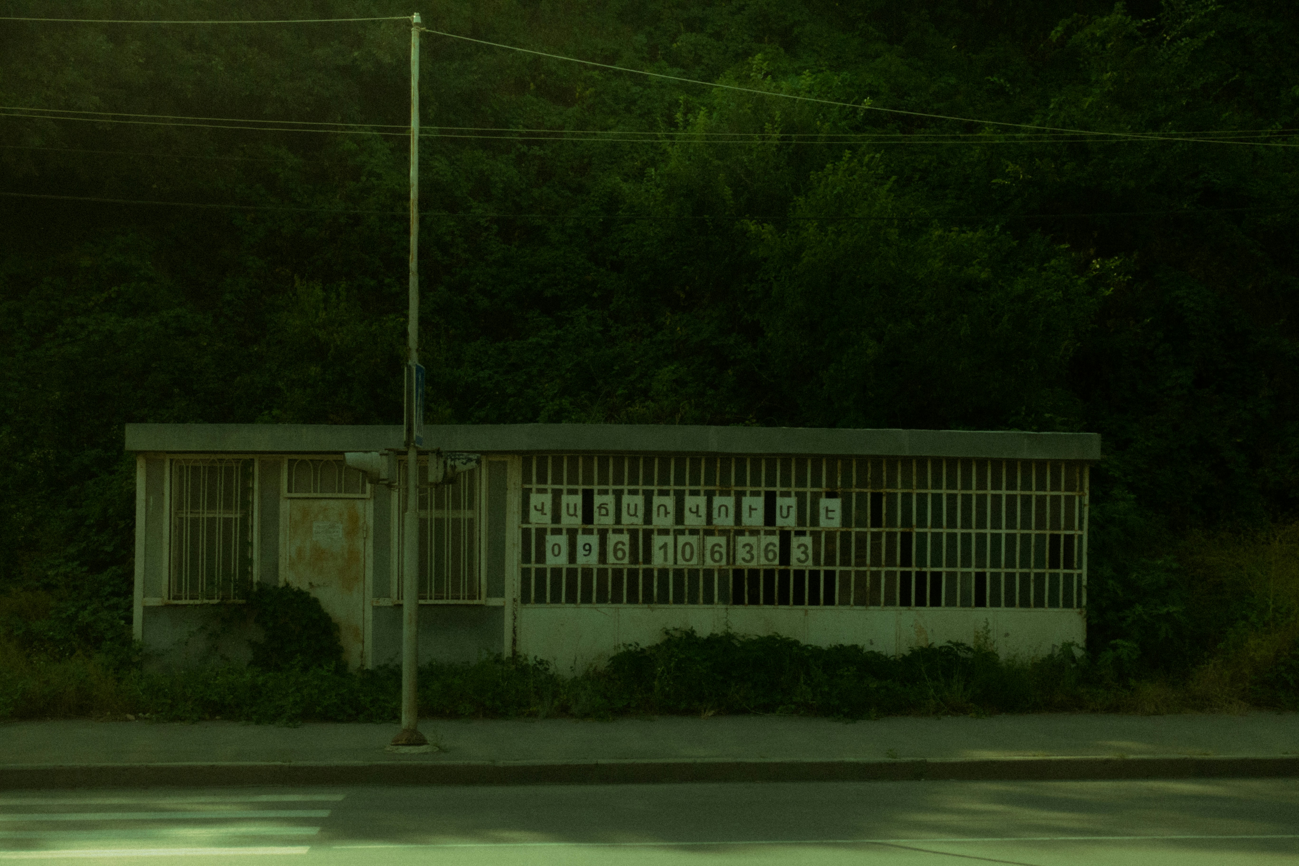 An old, weathered building with a grid of numbers on its facade, surrounded by lush greenery. The scene evokes a sense of nostalgia and decay.
