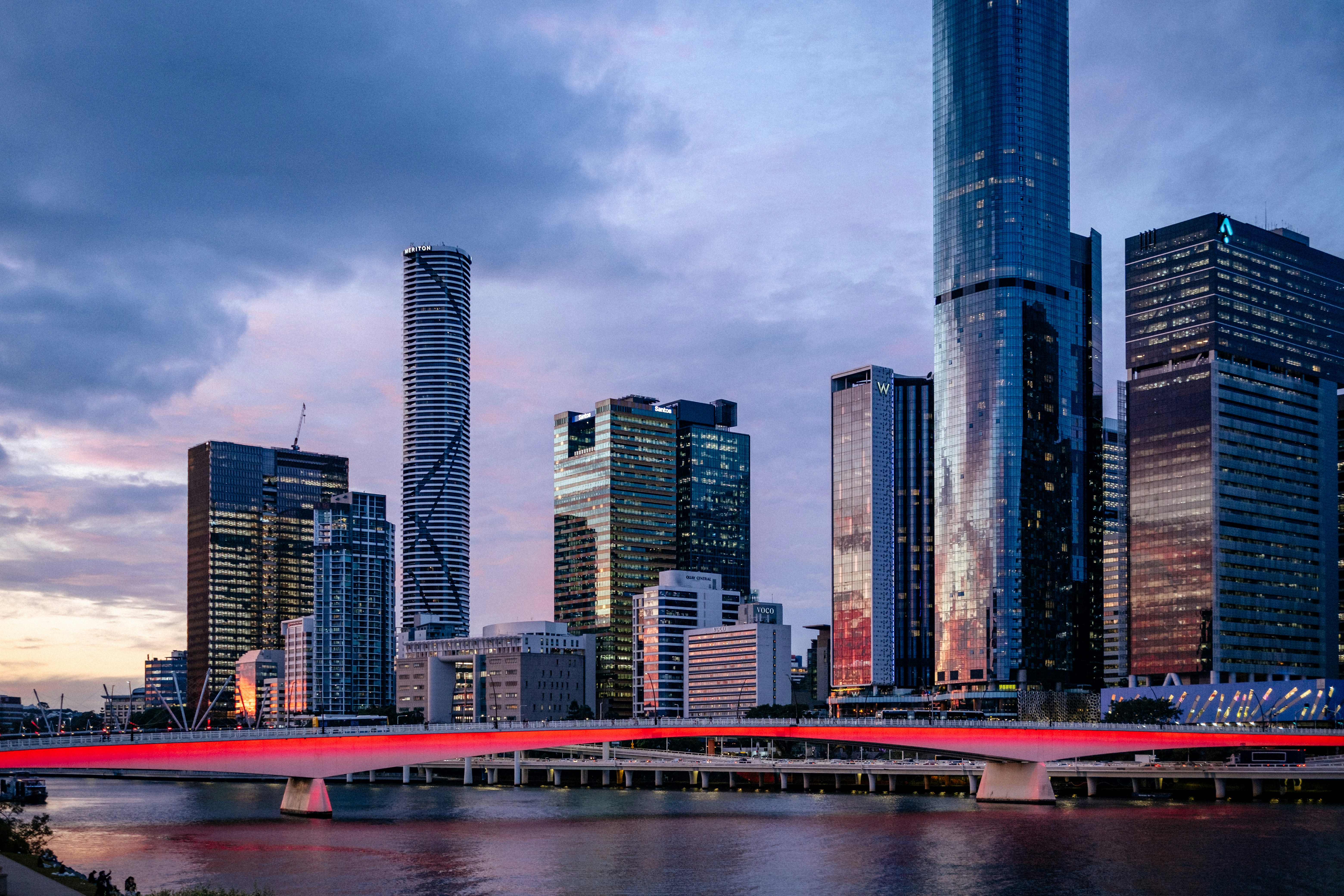 Skyscrapers tower over a river at dusk.