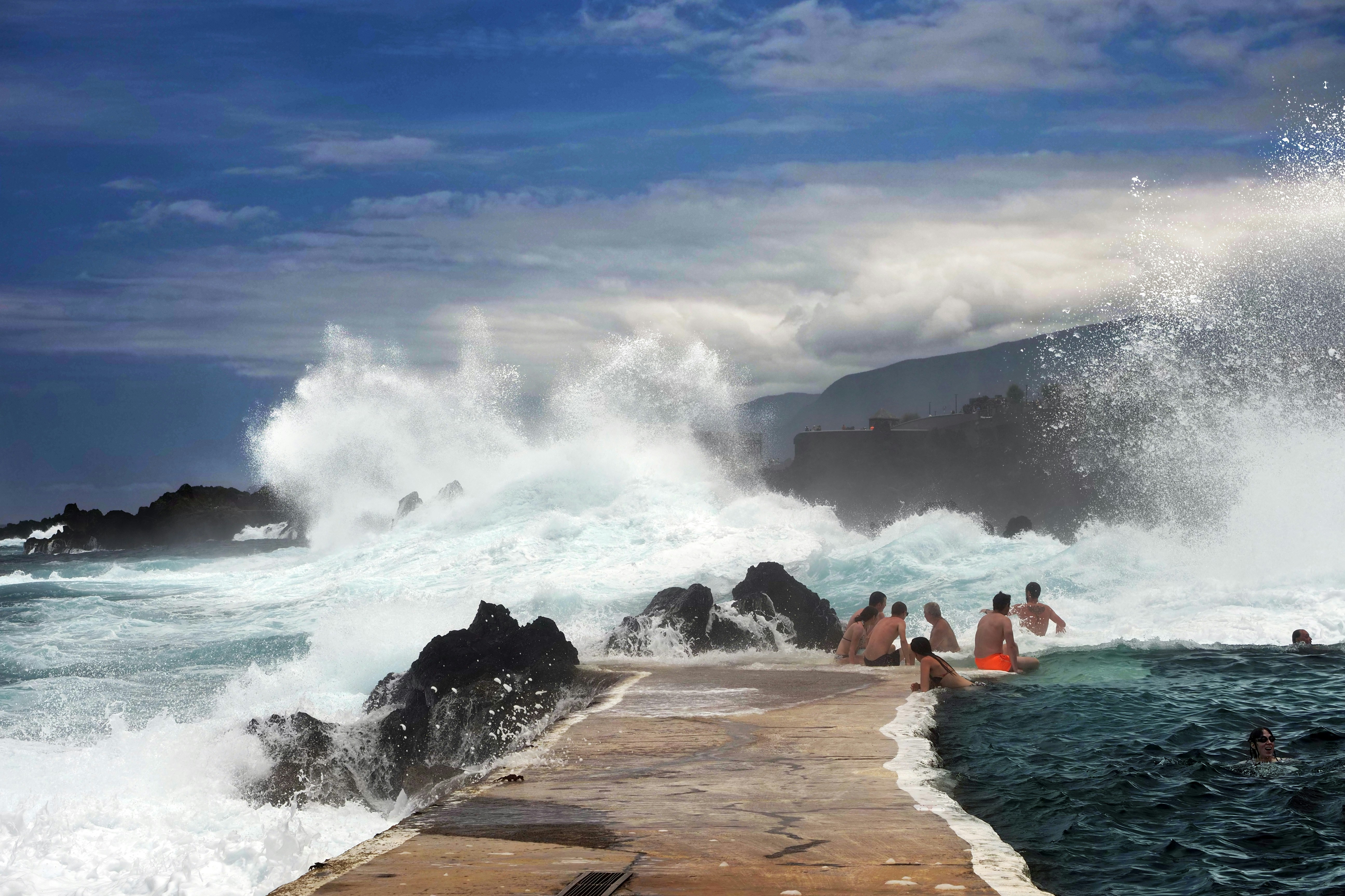 Surfers navigating the waves near a rocky jetty as powerful surf crashes around them.