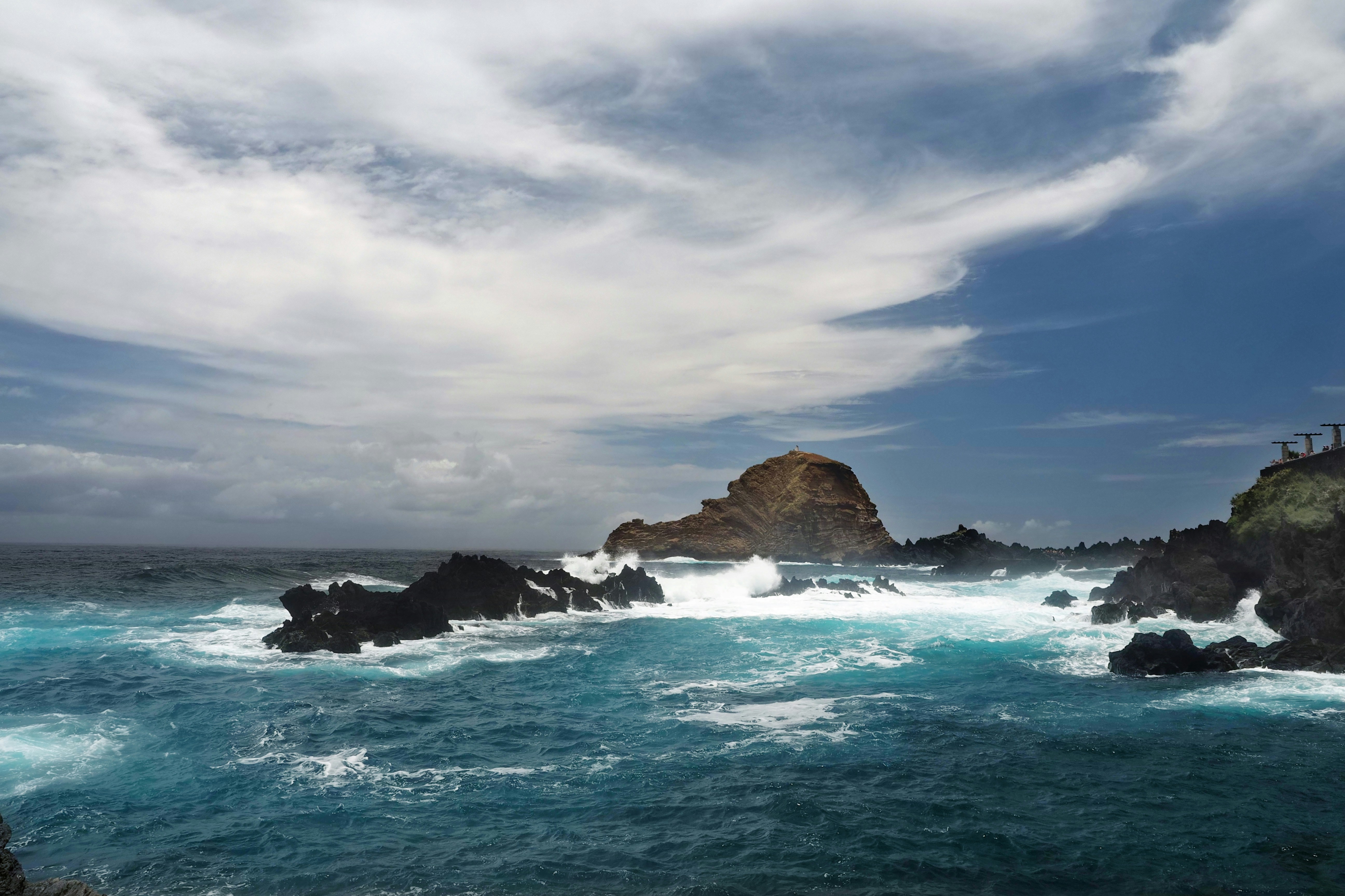 Waves crash against rocks under a cloudy sky.
