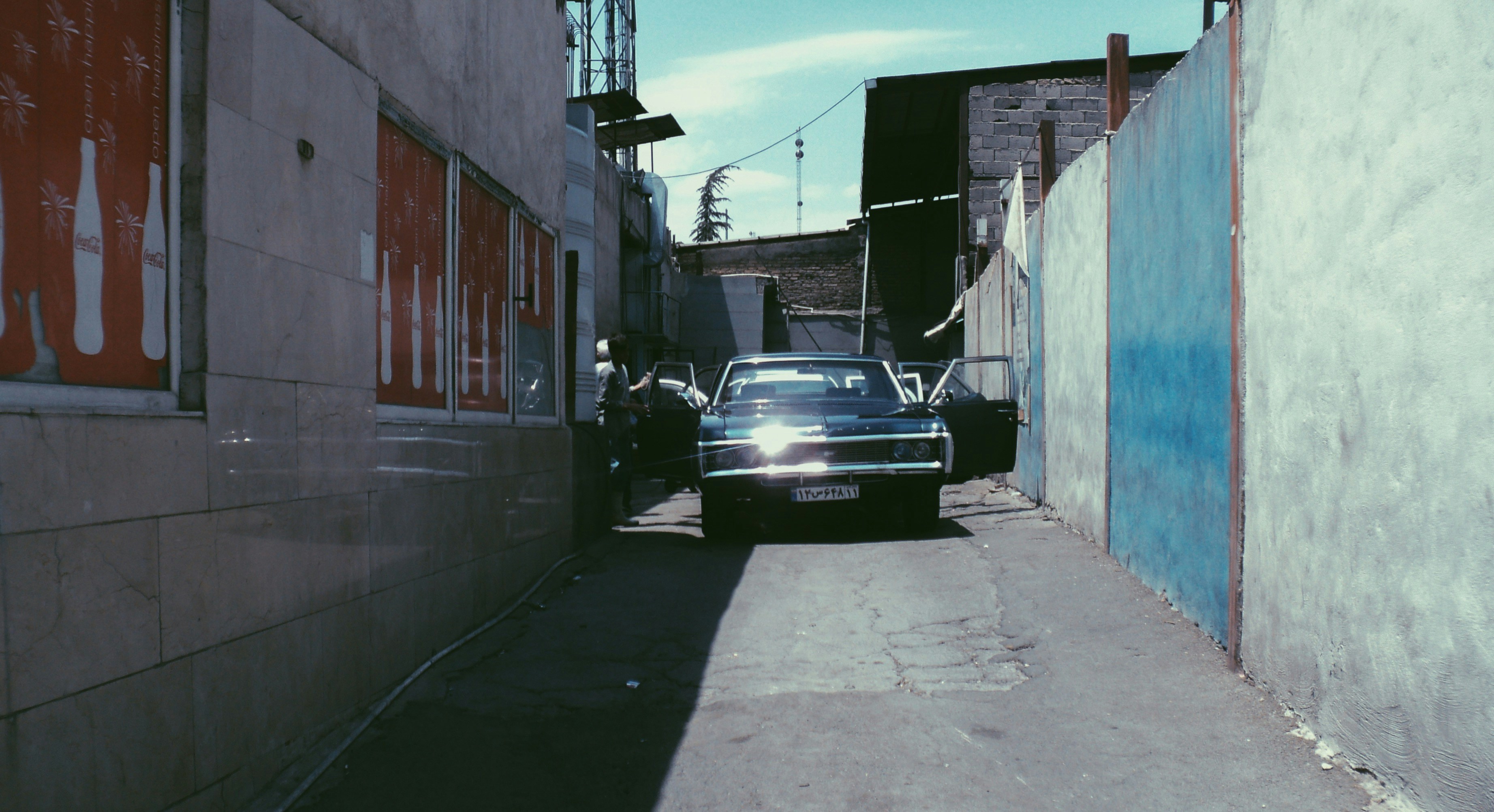 Classic car parked in a narrow alleyway, flanked by colorful walls and urban textures.