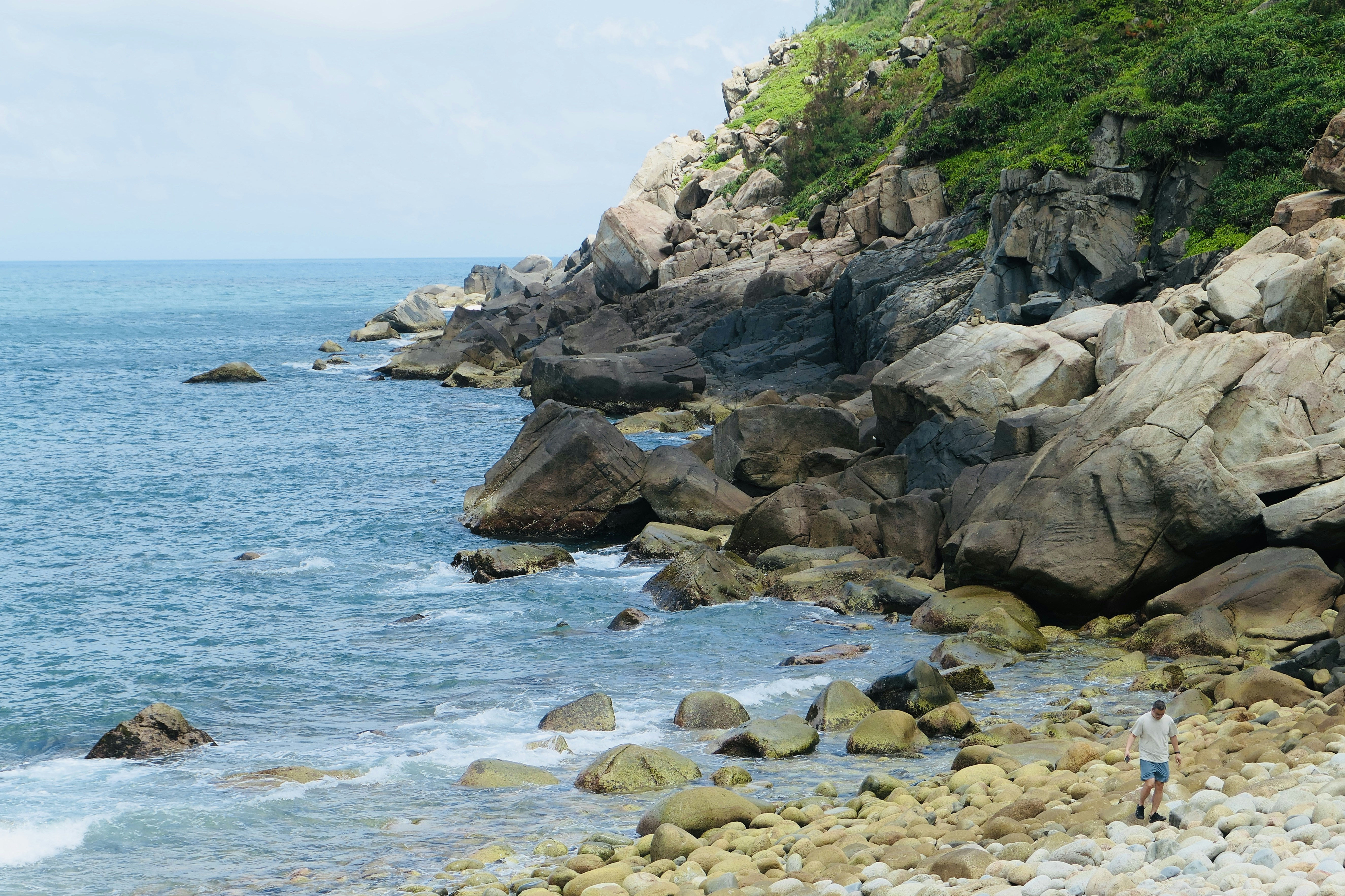Rocky coast meets the ocean under a bright sky.