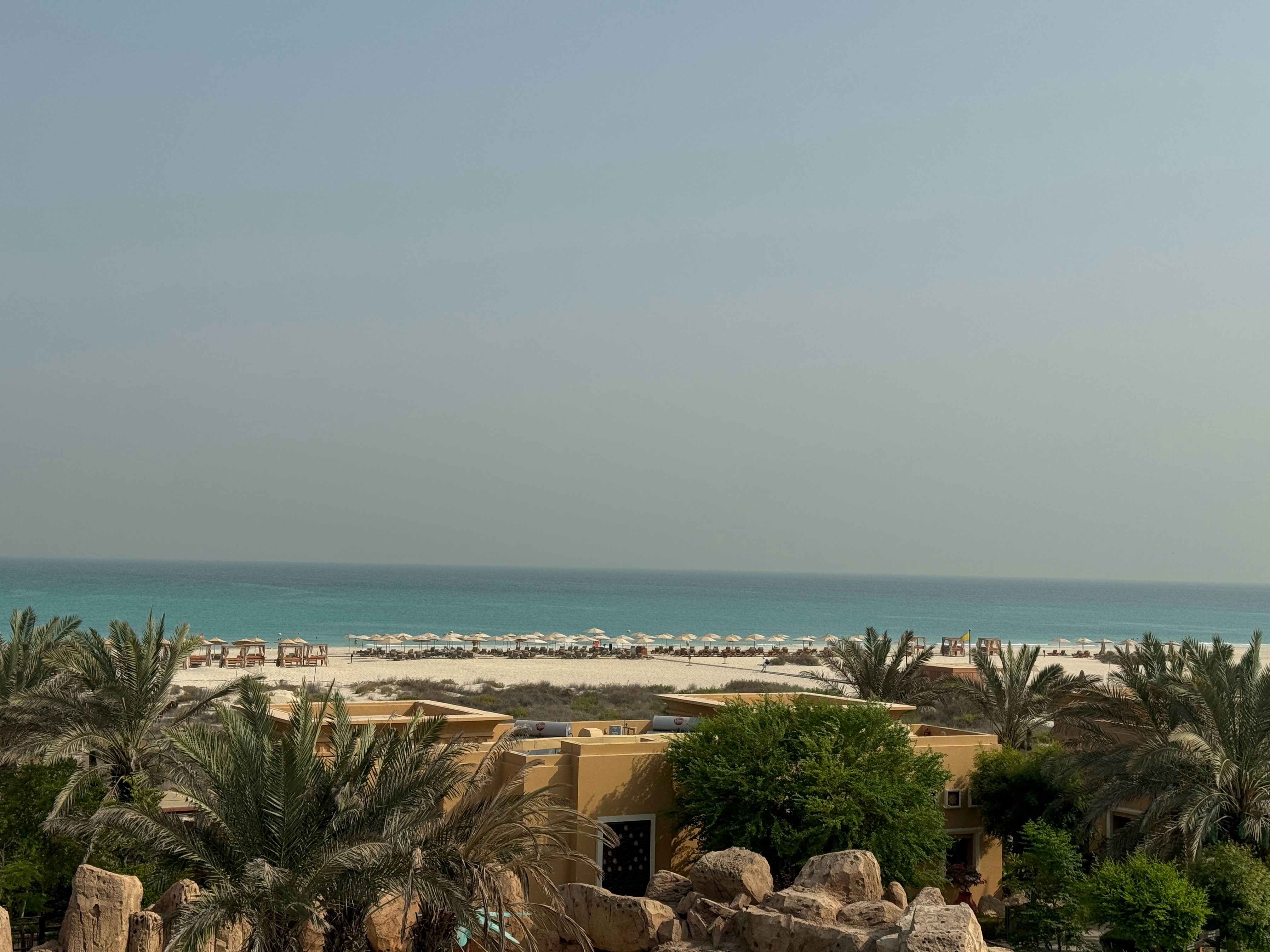 Beautiful Beach in Abu Dhabi UAE, Luxury Travel | Beach, palm trees, and resort under a hazy sky.