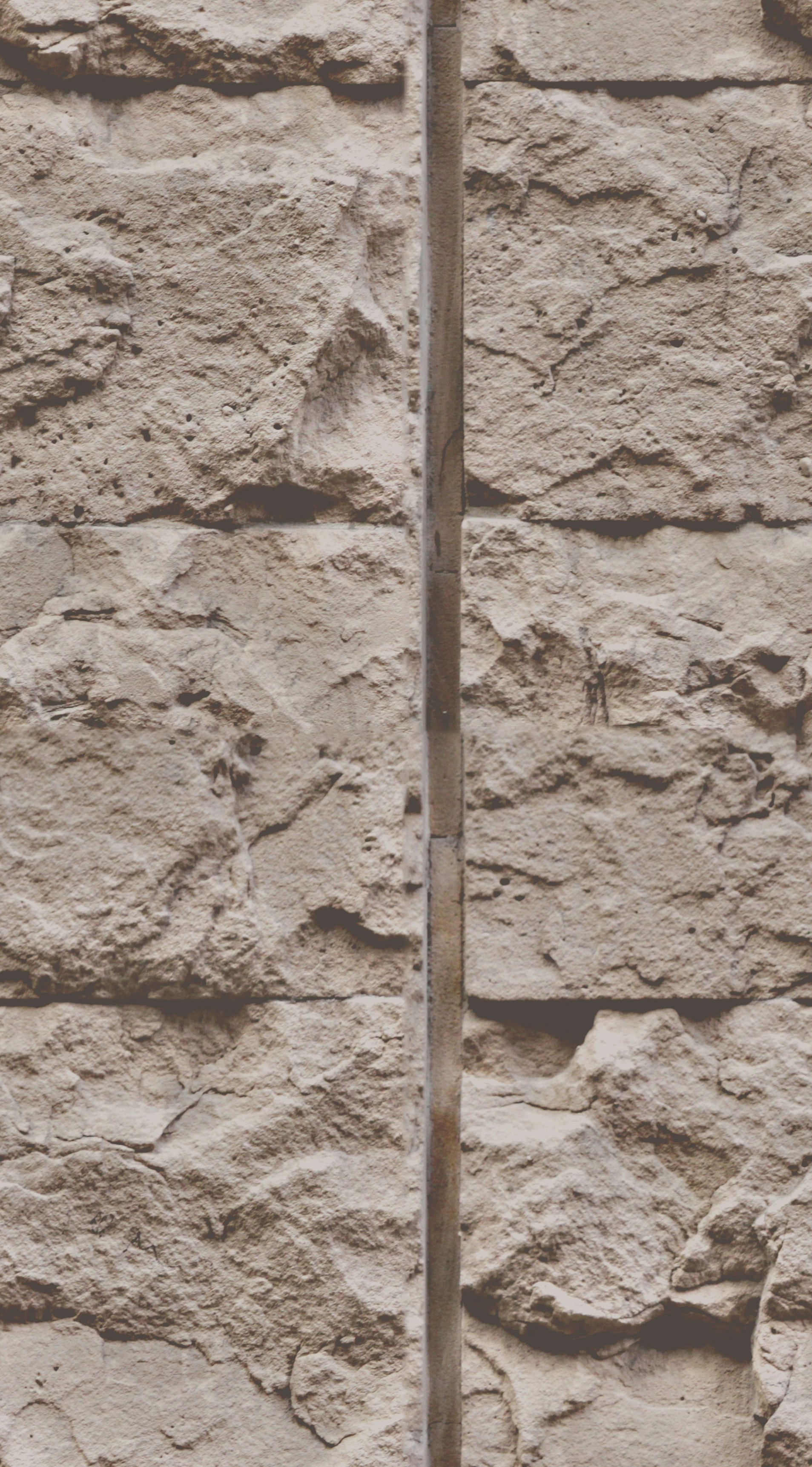 A close-up of a weathered, textured brick wall with a vertical wooden post running through it. | Stone wall with a vertical seam.