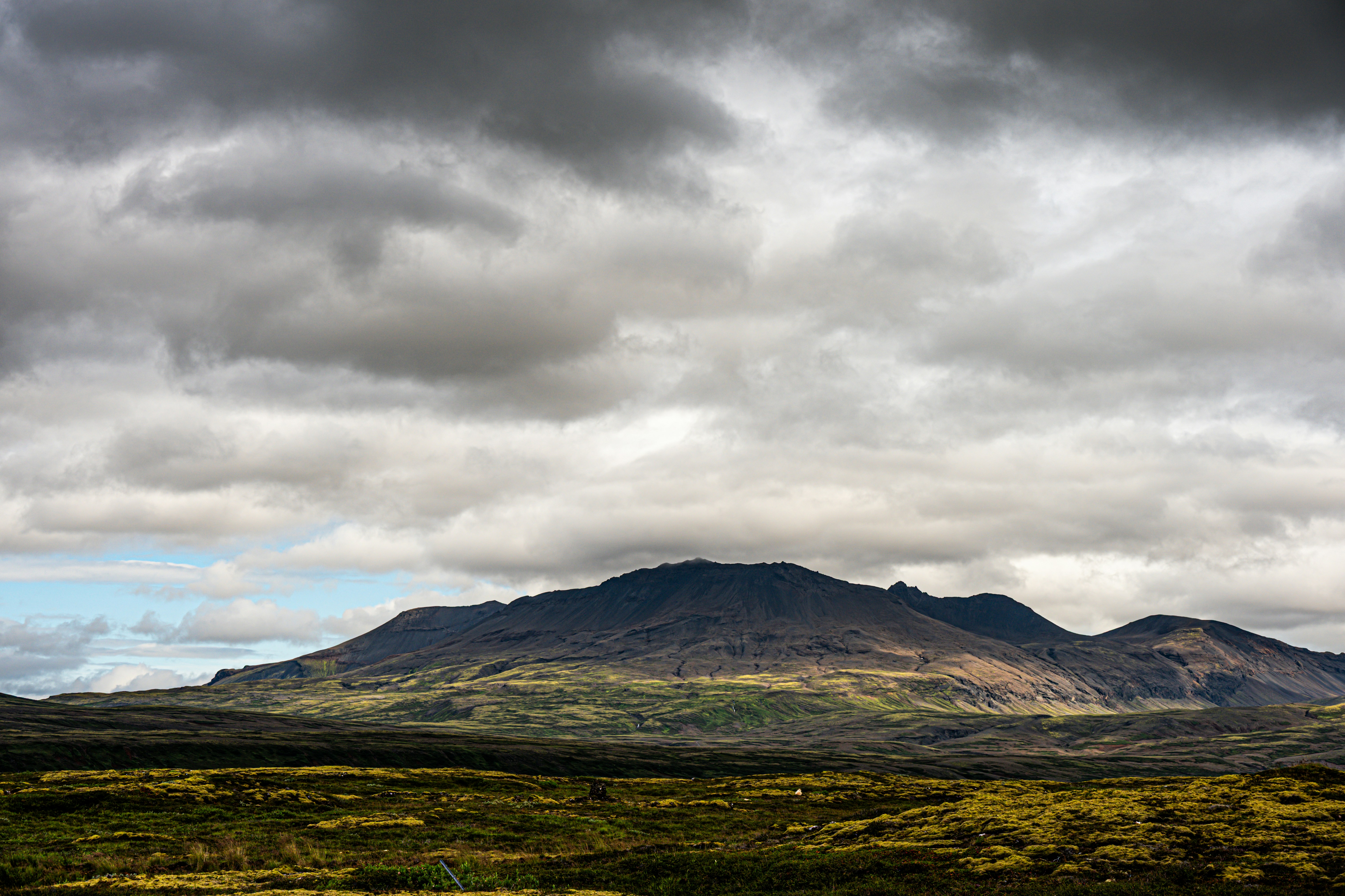 A rugged mountain rises against a backdrop of dramatic clouds, showcasing the serene yet powerful essence of the highlands. Lush greenery blankets the foreground.