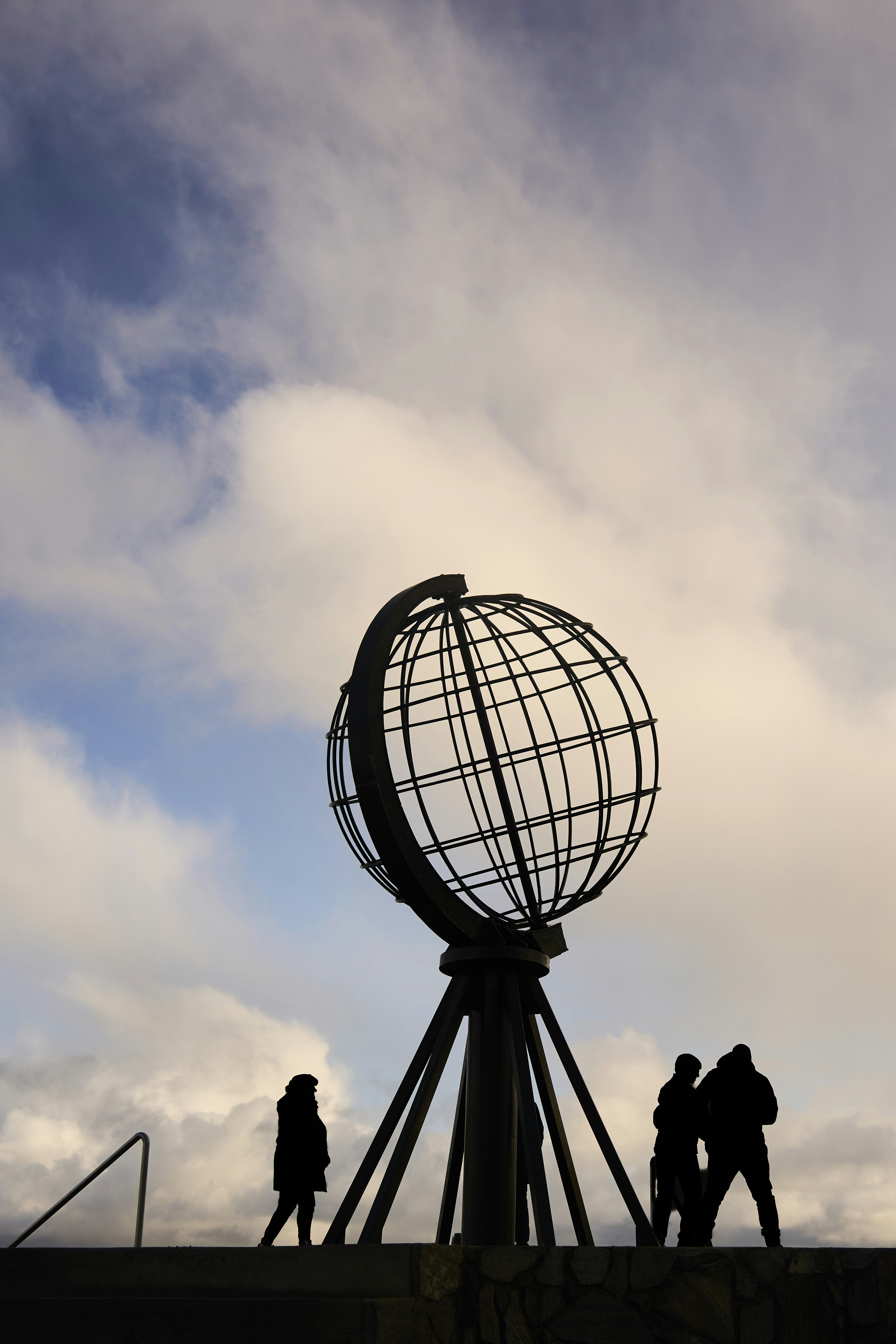 Nordkap, | People stand near a giant globe sculpture.
