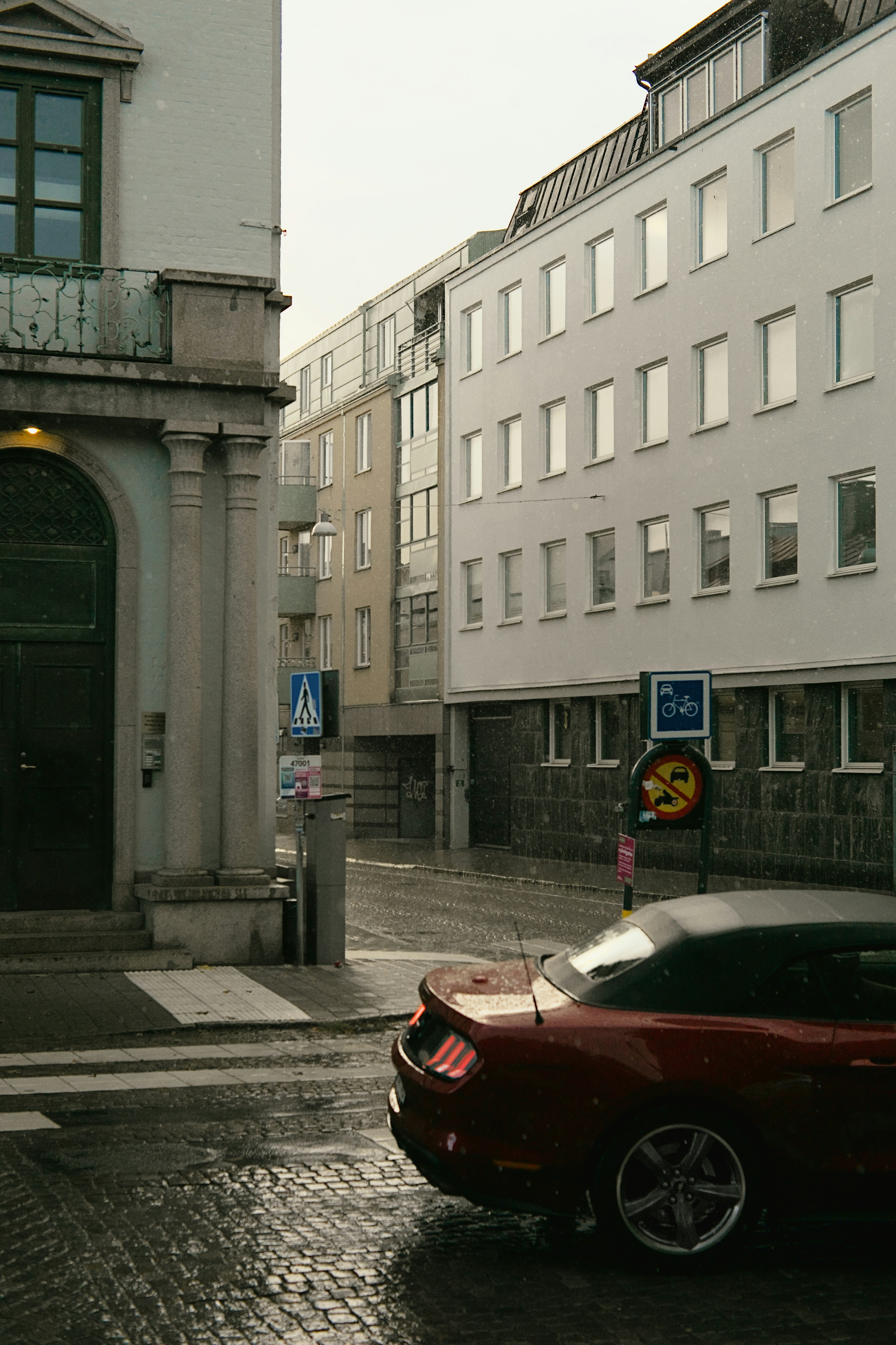 red mustang in the rainy summer day Växjö, Sweden | A red car is parked on a wet city street.