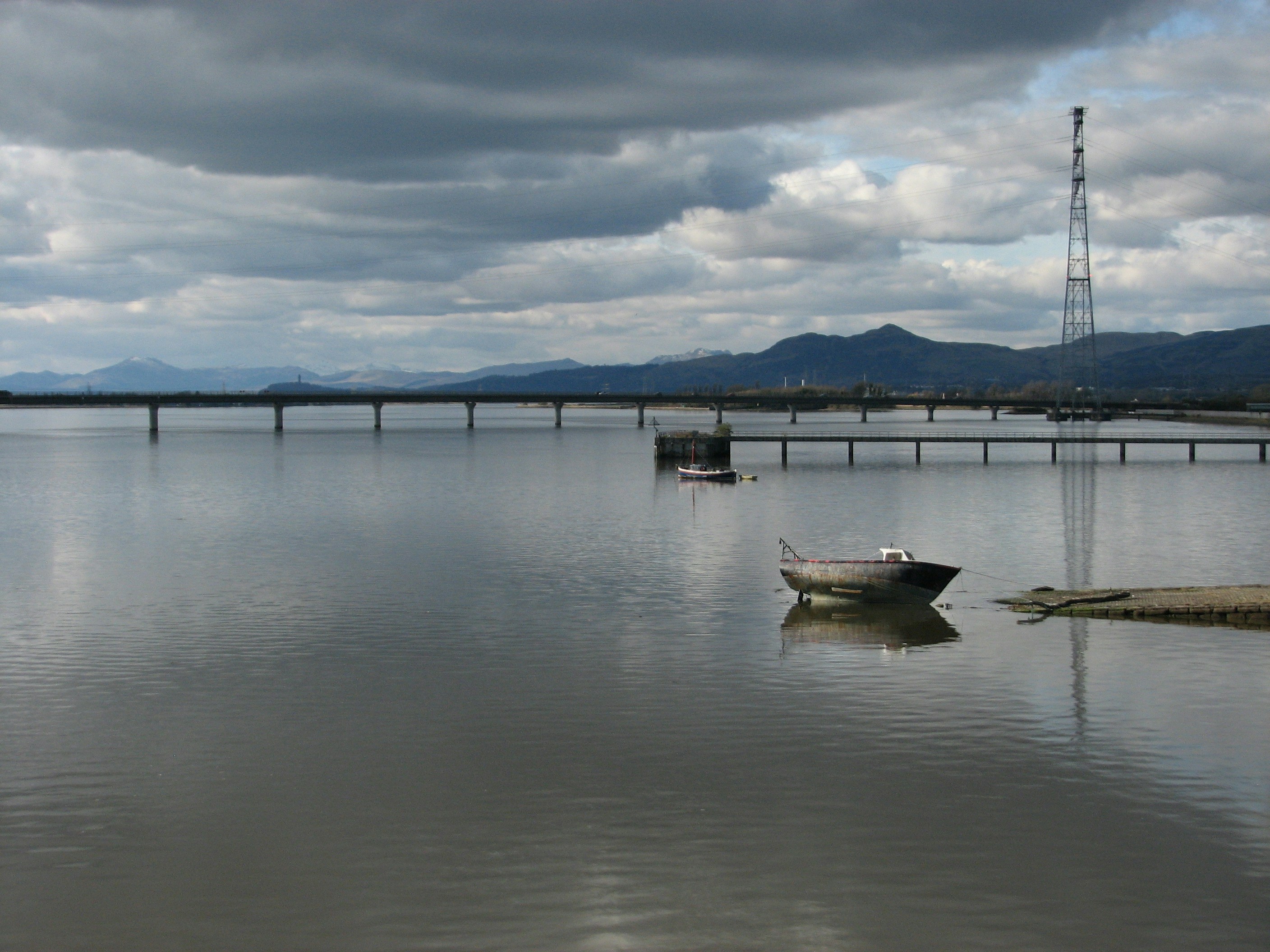 water landscape with small boats. Bridge and antenna in the background | A bridge spans over a calm river.