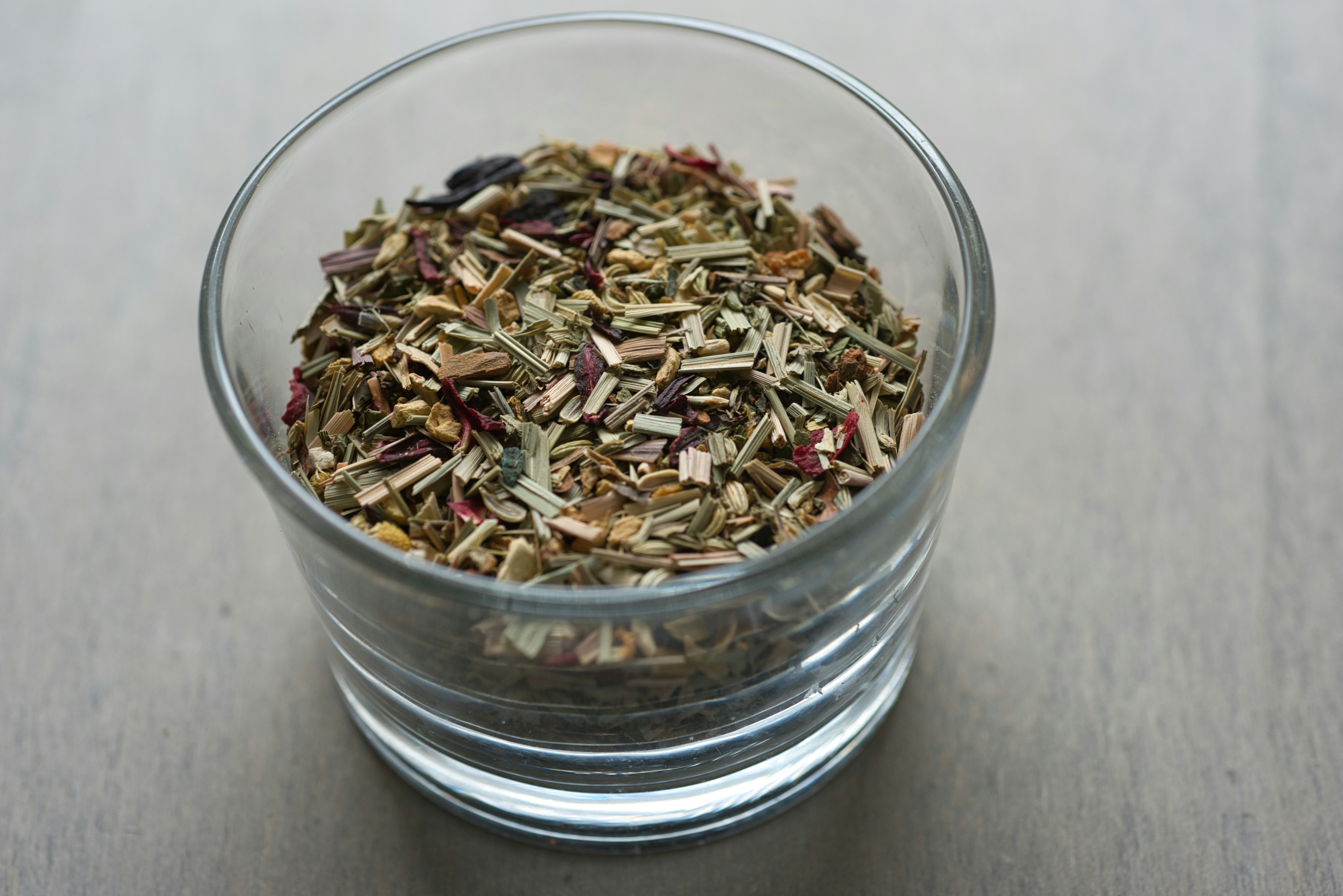 A close-up view of colorful spices neatly arranged in a transparent glass jar. The texture and tones highlight the variety and richness of the ingredients. | Herbal tea blend in a glass.