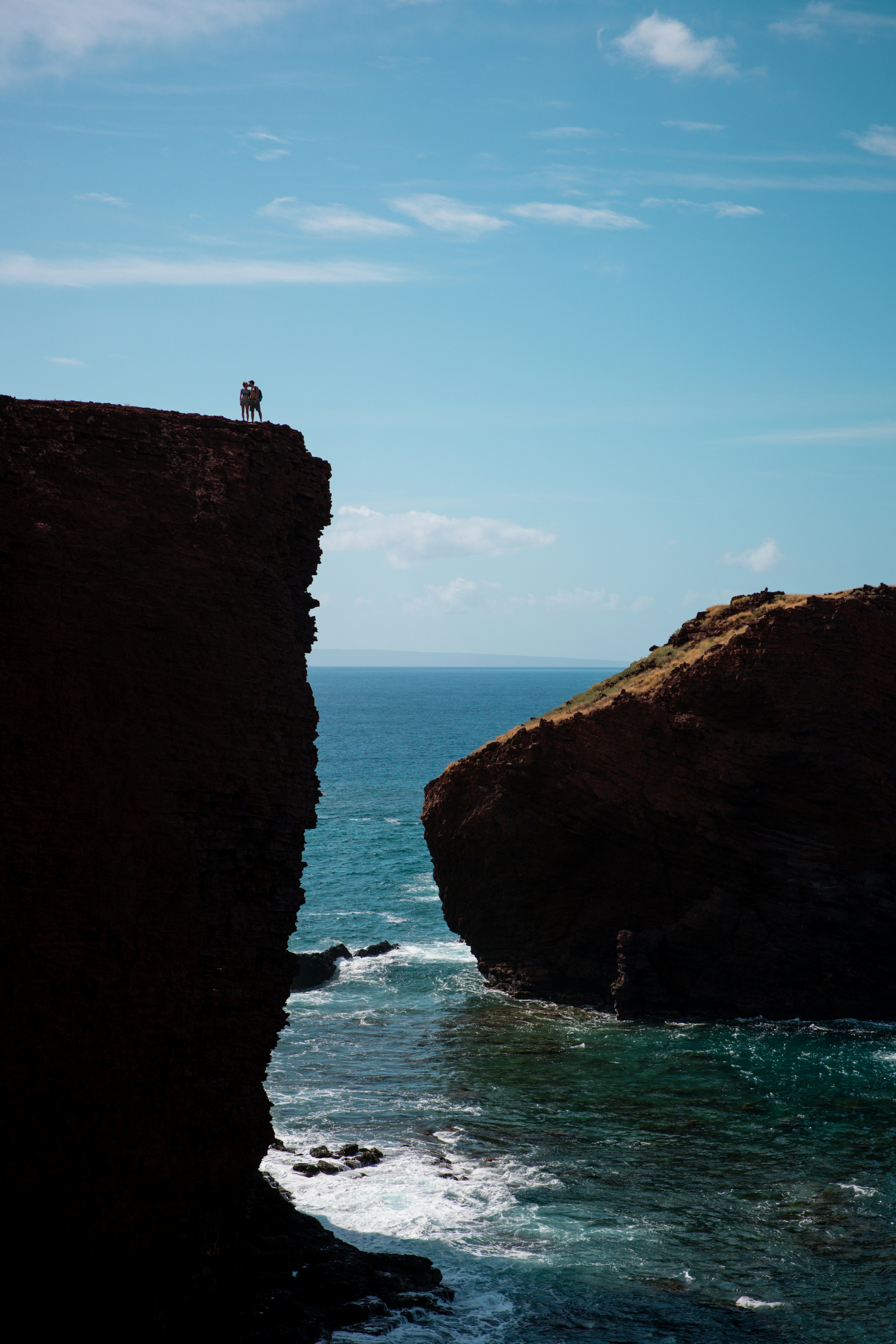 Cliff side of Lanai | Two people stand on a cliff overlooking the ocean.