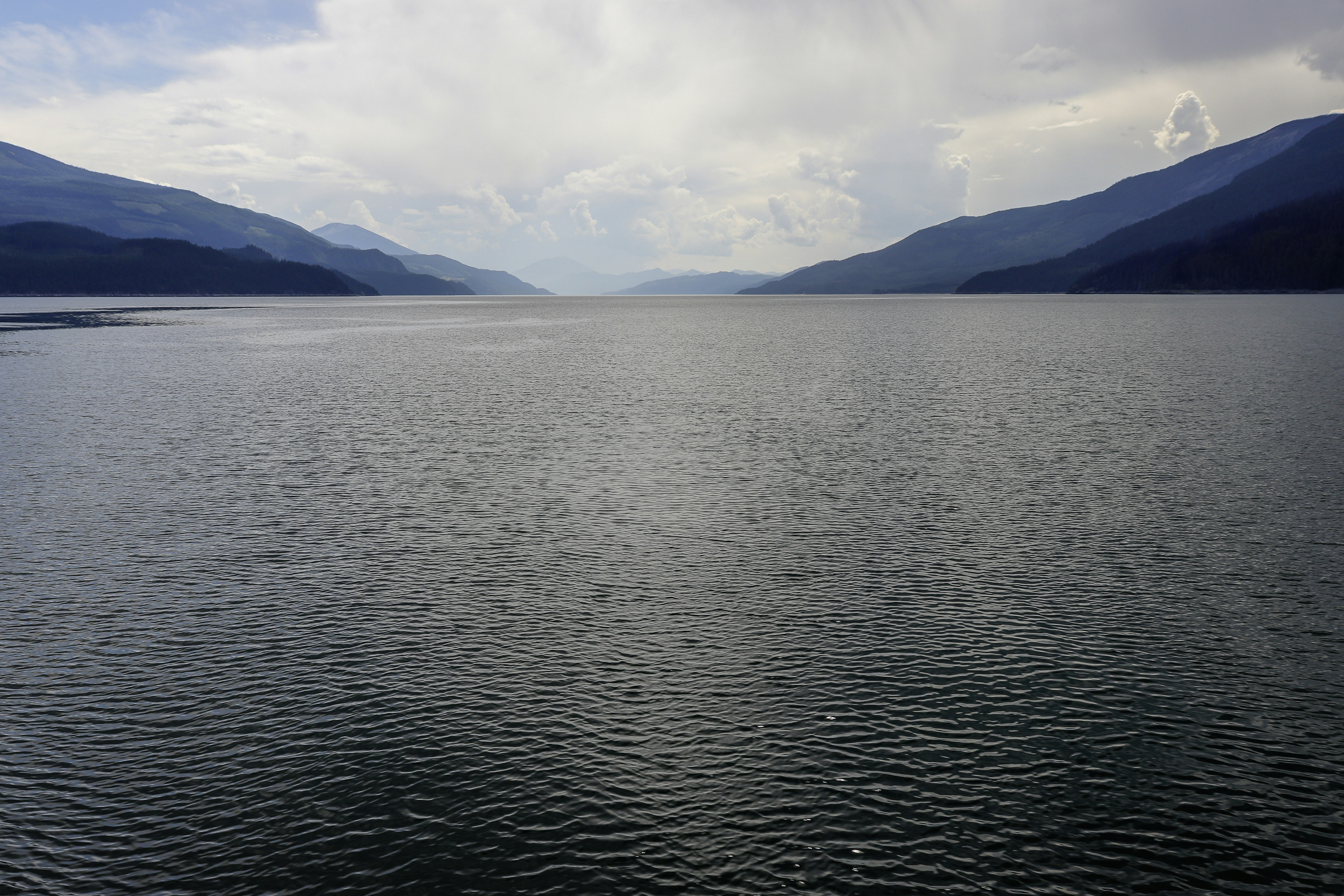 Canada British Columbia Selkirk Mountain Ranges Upper and Lower Arrow Lake ferries. | A calm lake lies between distant mountains.