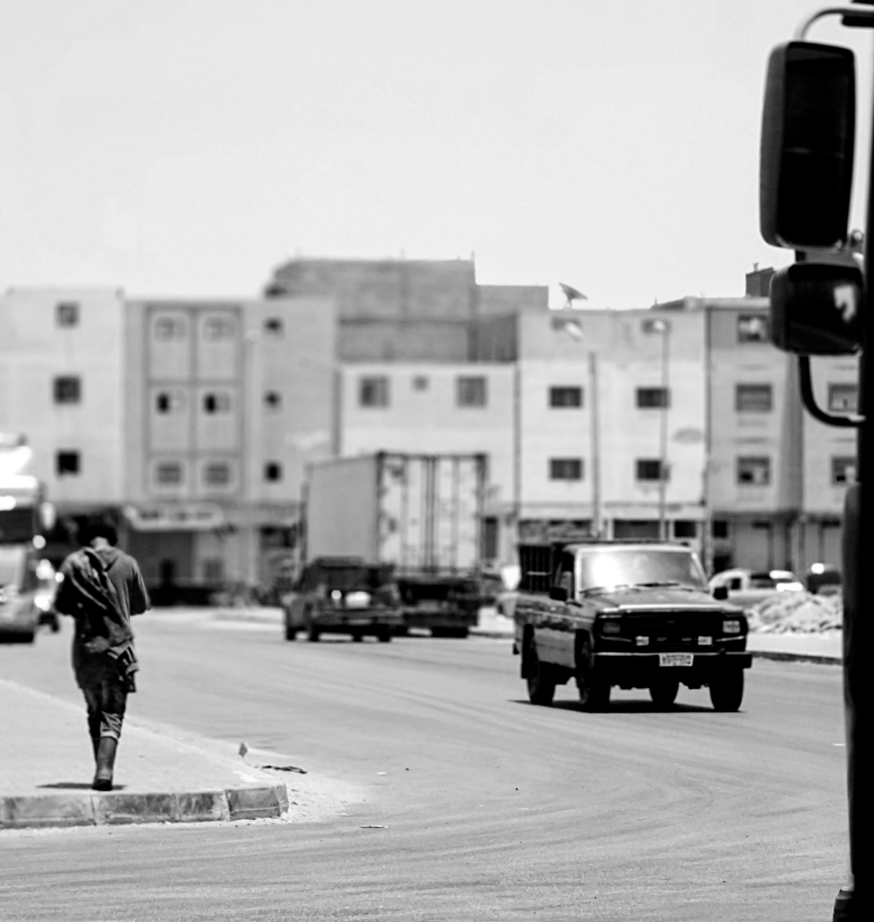 A person walks by cars and buildings.