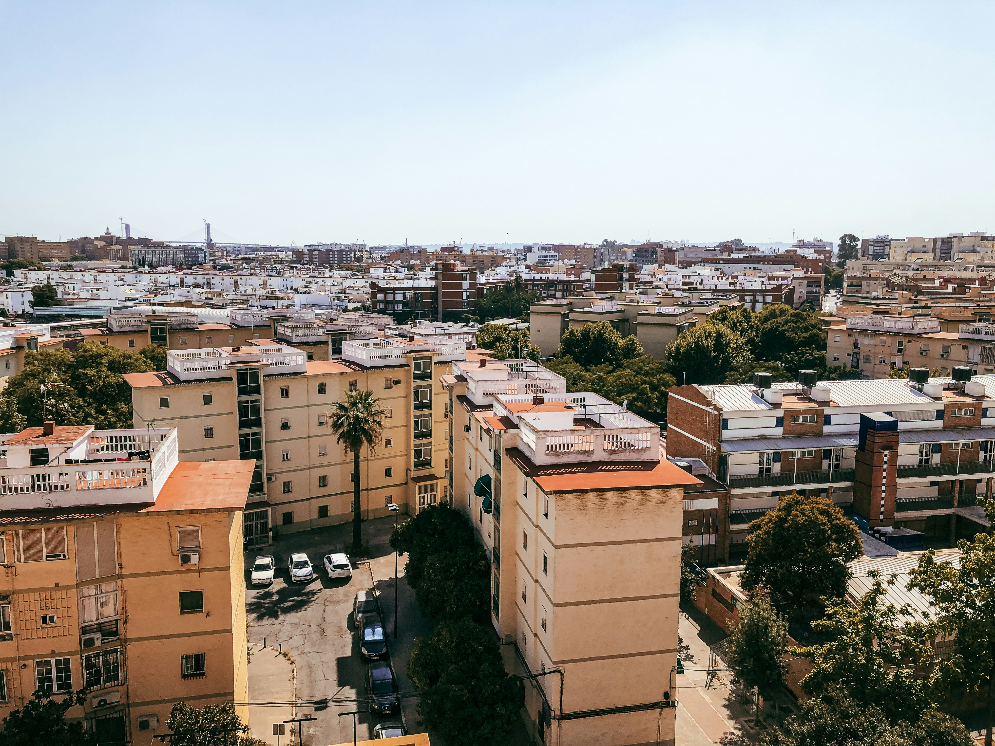 Aerial view of a residential area showcasing a mix of buildings and greenery, with a distant skyline under a clear blue sky.