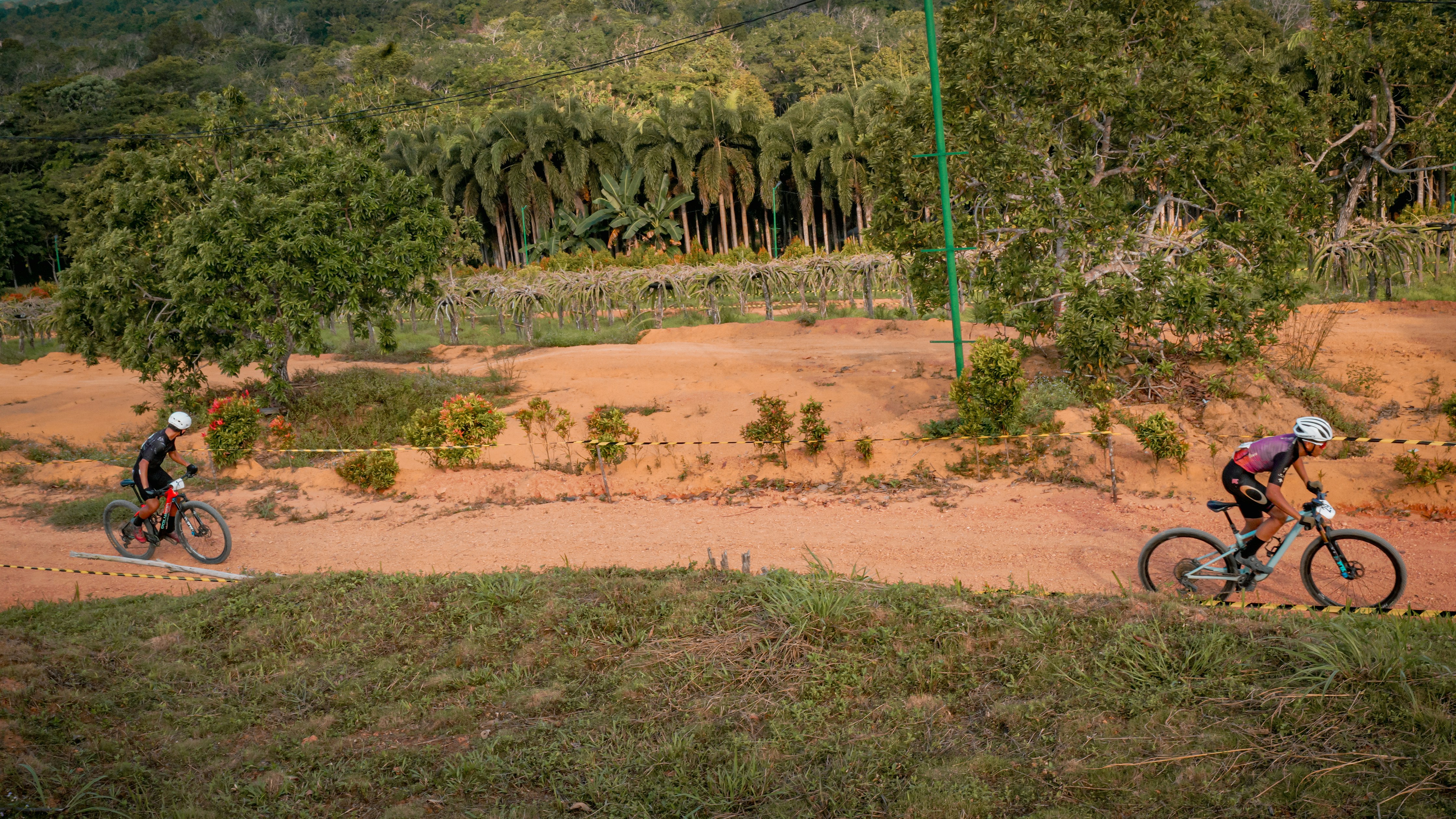 Two cyclists ride mountain bikes on a dirt track.