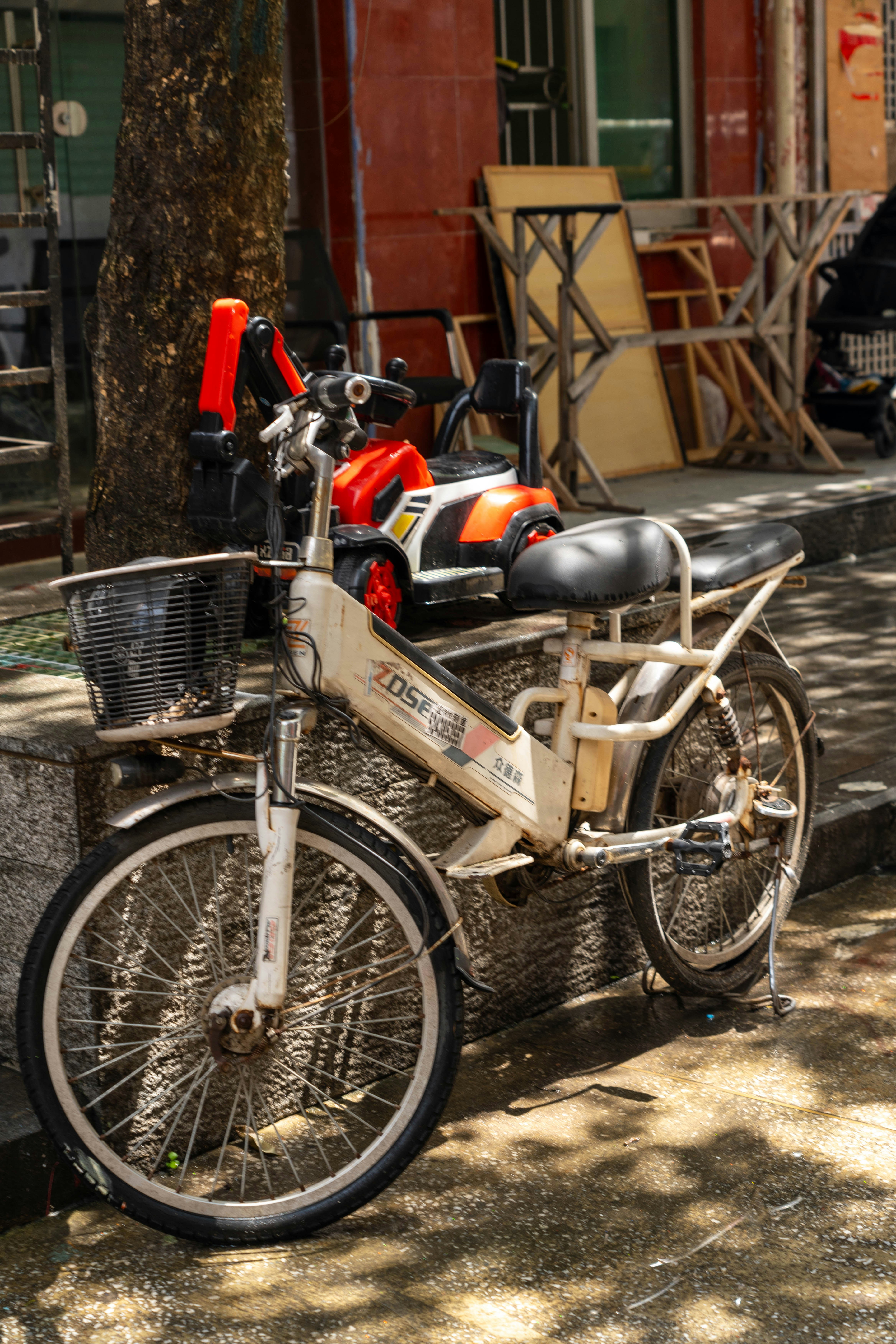Electric bicycle parked beside a tree on a bustling street, showcasing urban mobility. The scene captures the essence of city life.