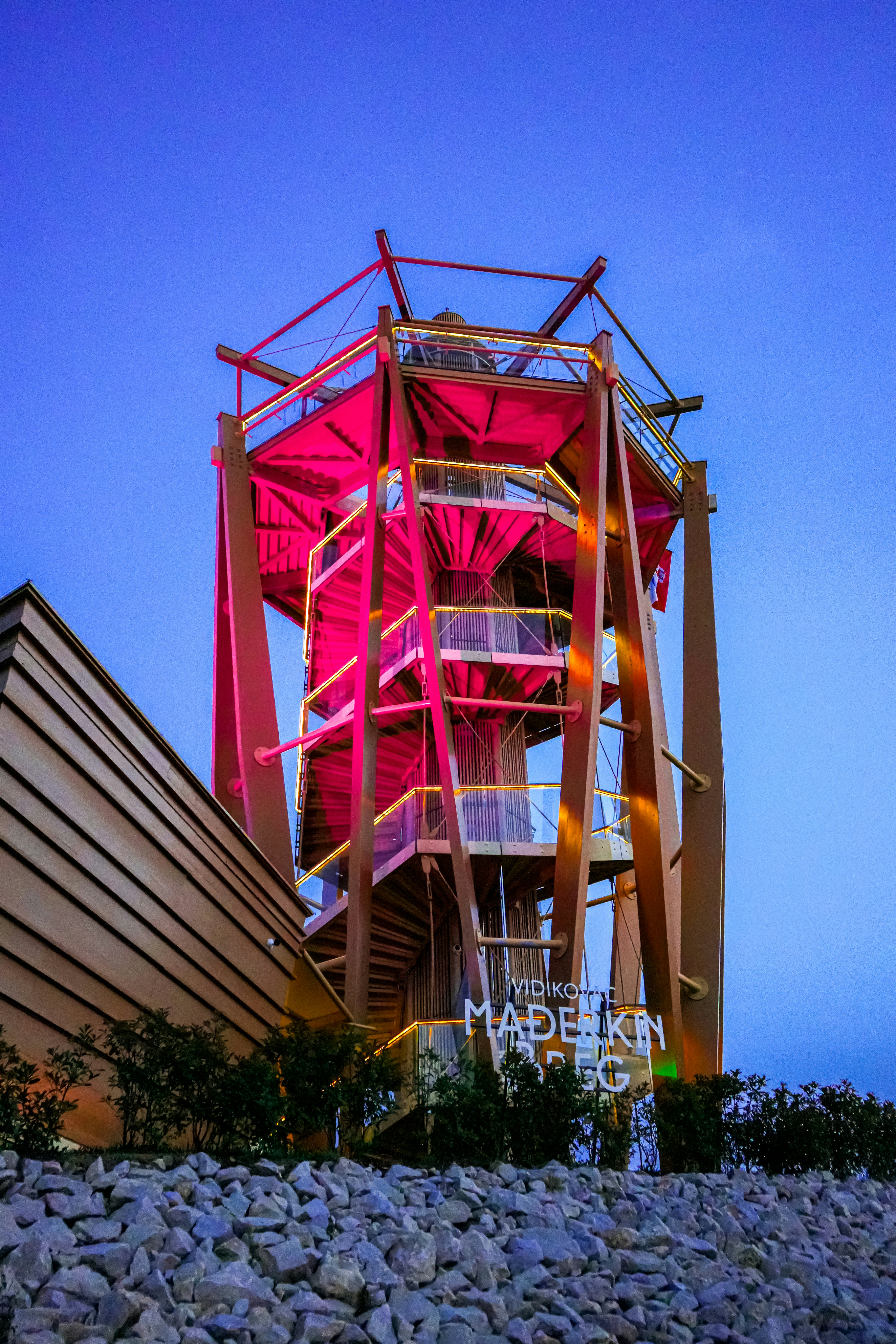 A striking observation tower illuminated in pink hues, set against a twilight sky, showcasing contemporary architectural design.