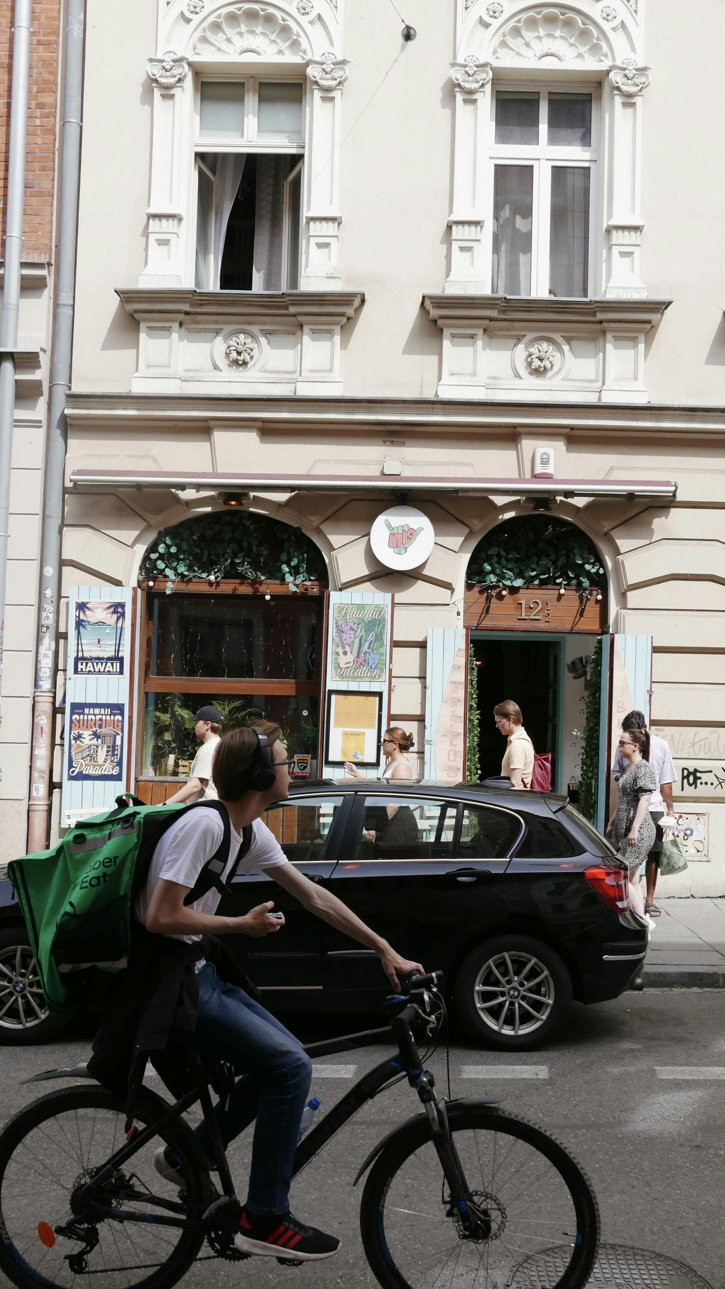 A cyclist passes by a lively street adorned with charming storefronts, where pedestrians engage with their surroundings. The scene captures the essence of urban activity.