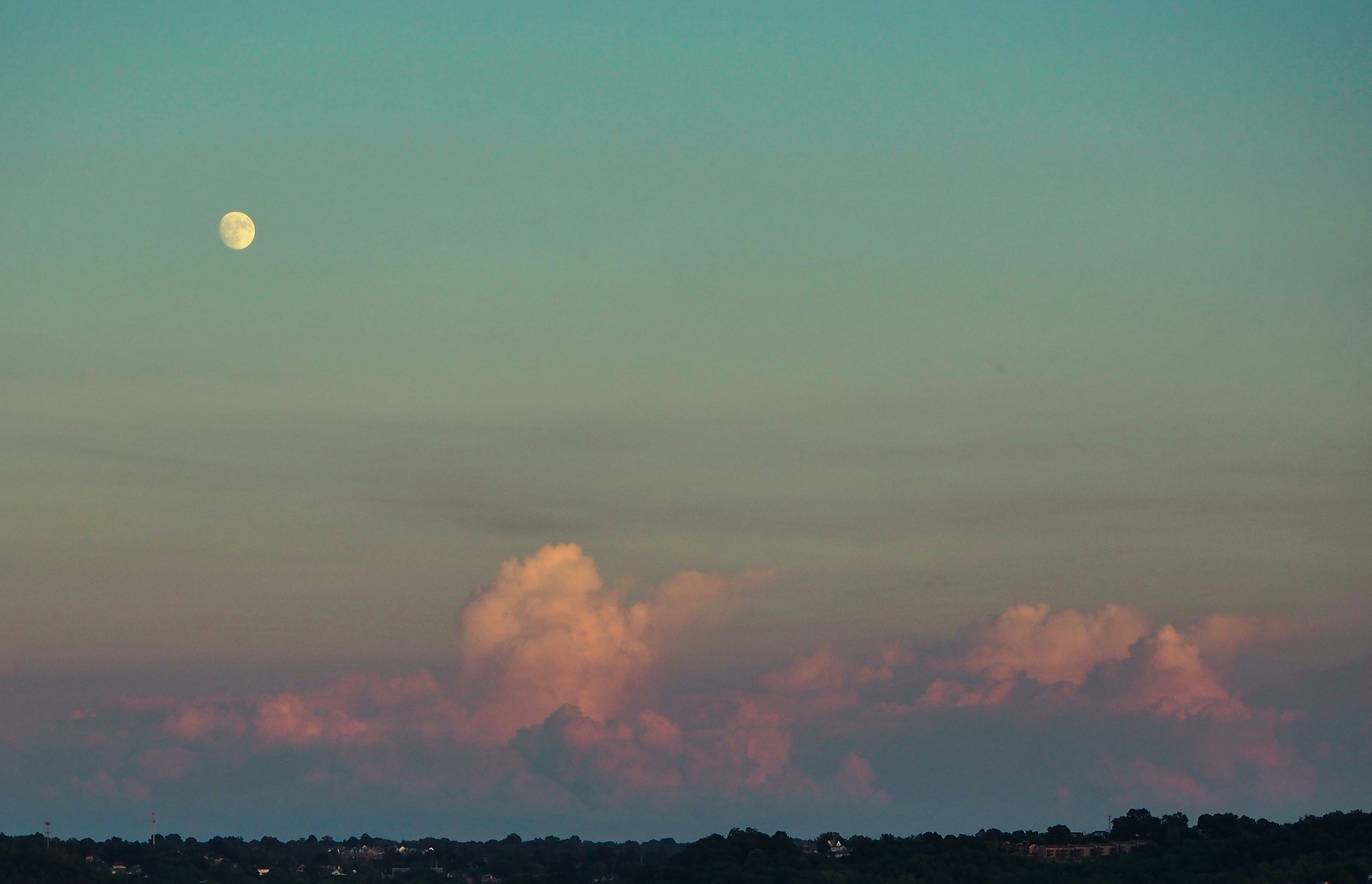 A luminous moon hangs in a pastel sky, casting gentle light over soft, billowing clouds at twilight.