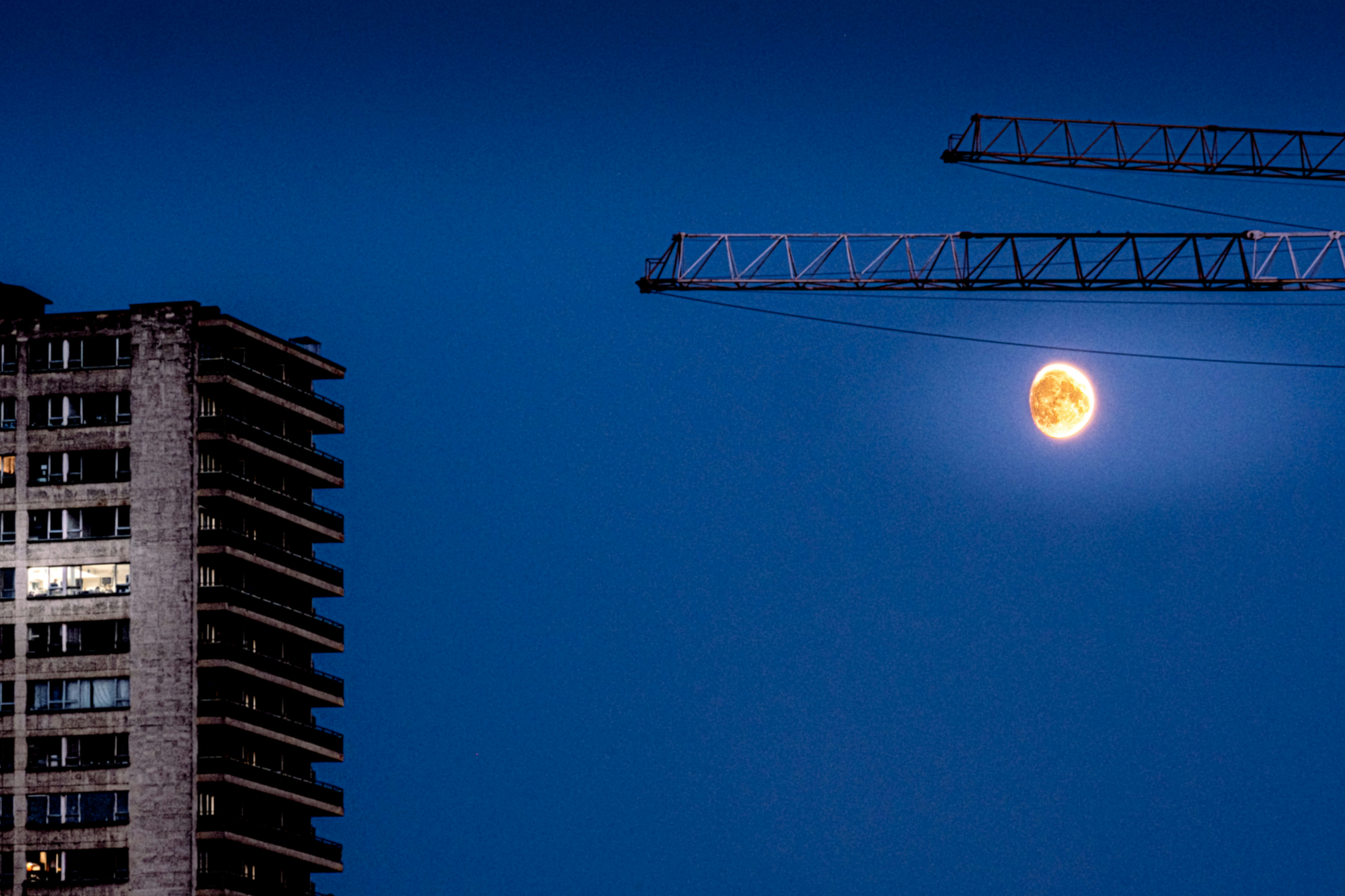 A moon shines bright over buildings at night.