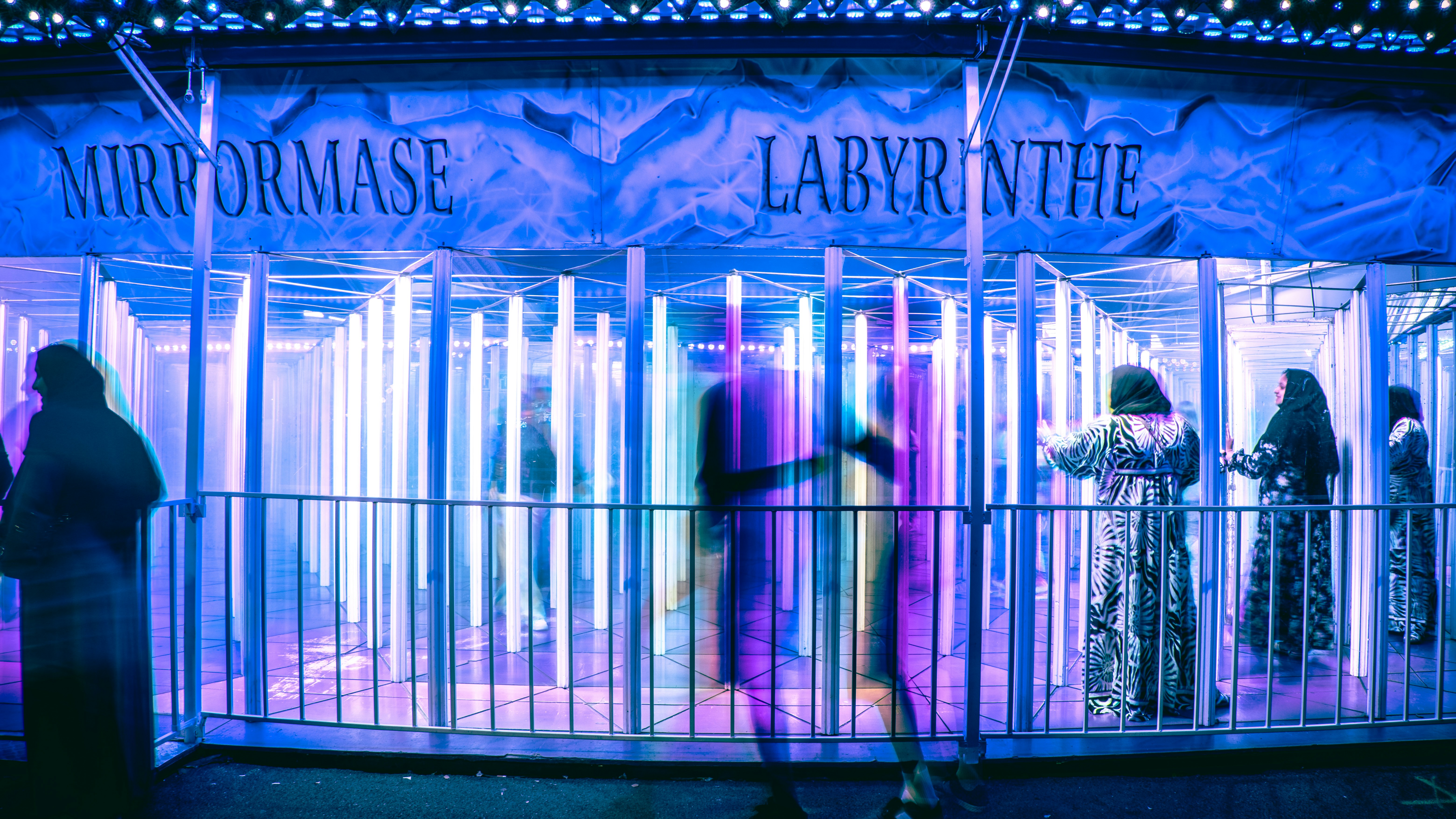 People are inside a neon-lit mirror maze.