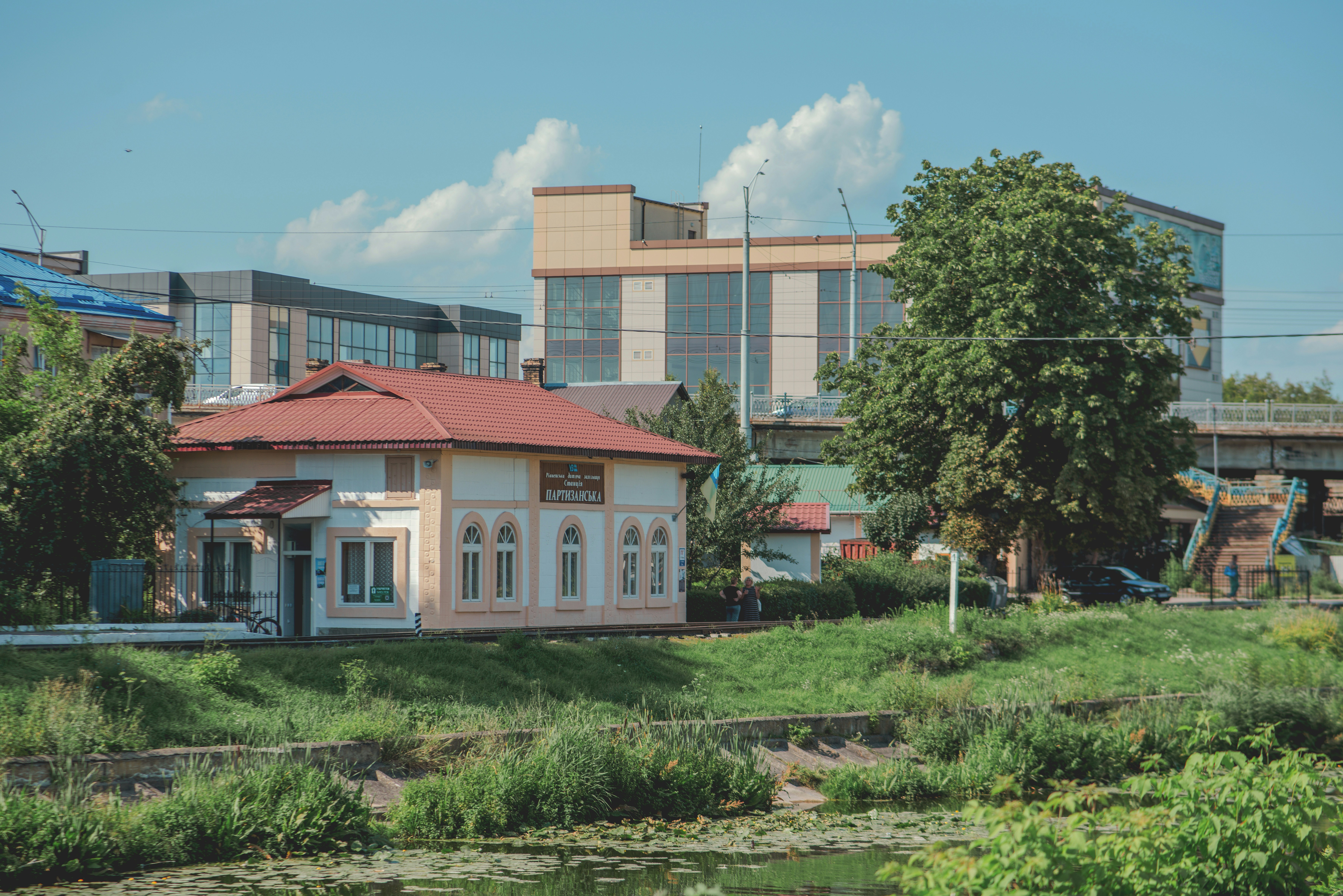 Charming historic building juxtaposed against contemporary architecture, surrounded by lush greenery and a tranquil waterway.