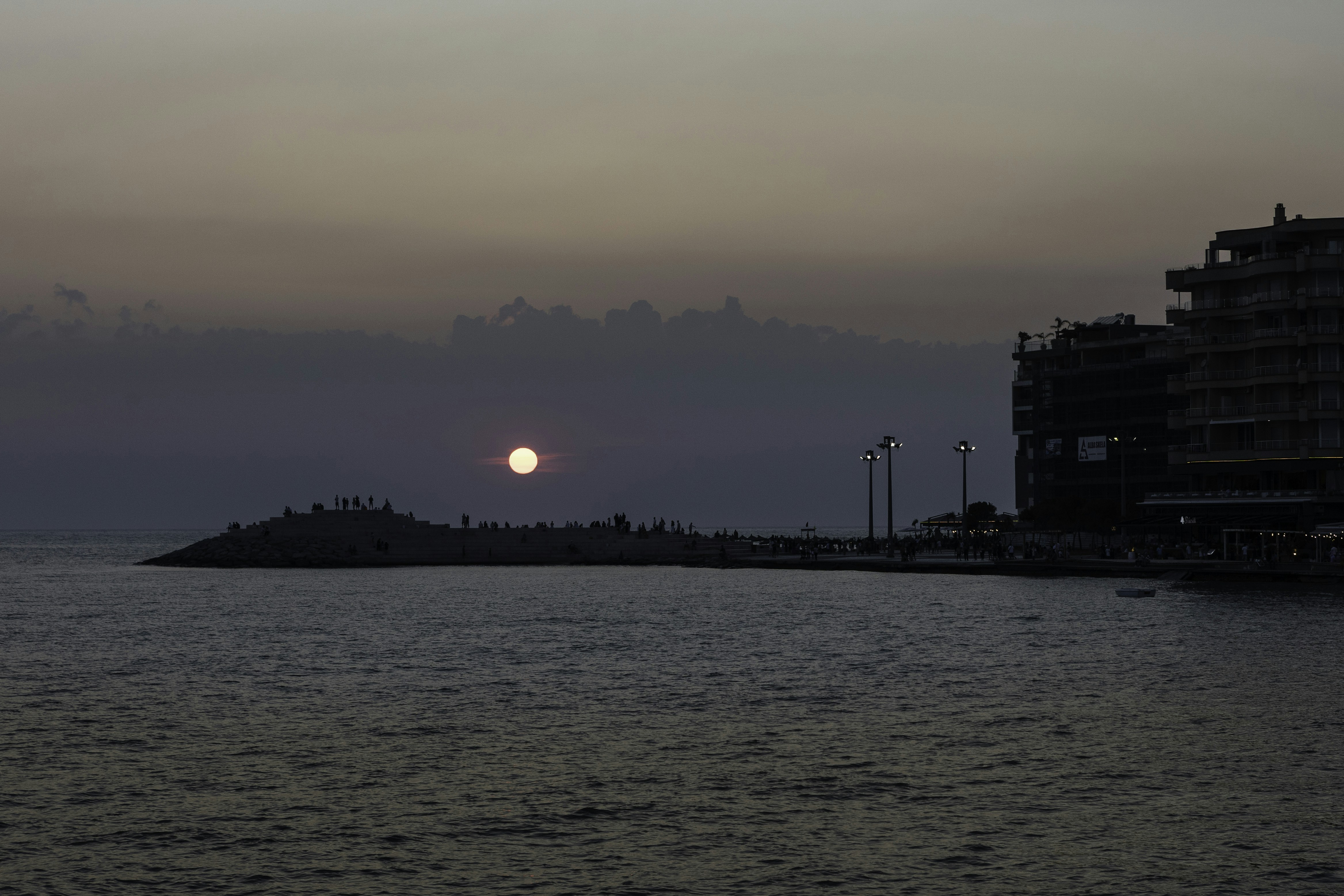 Sunset over the sea with buildings in view.