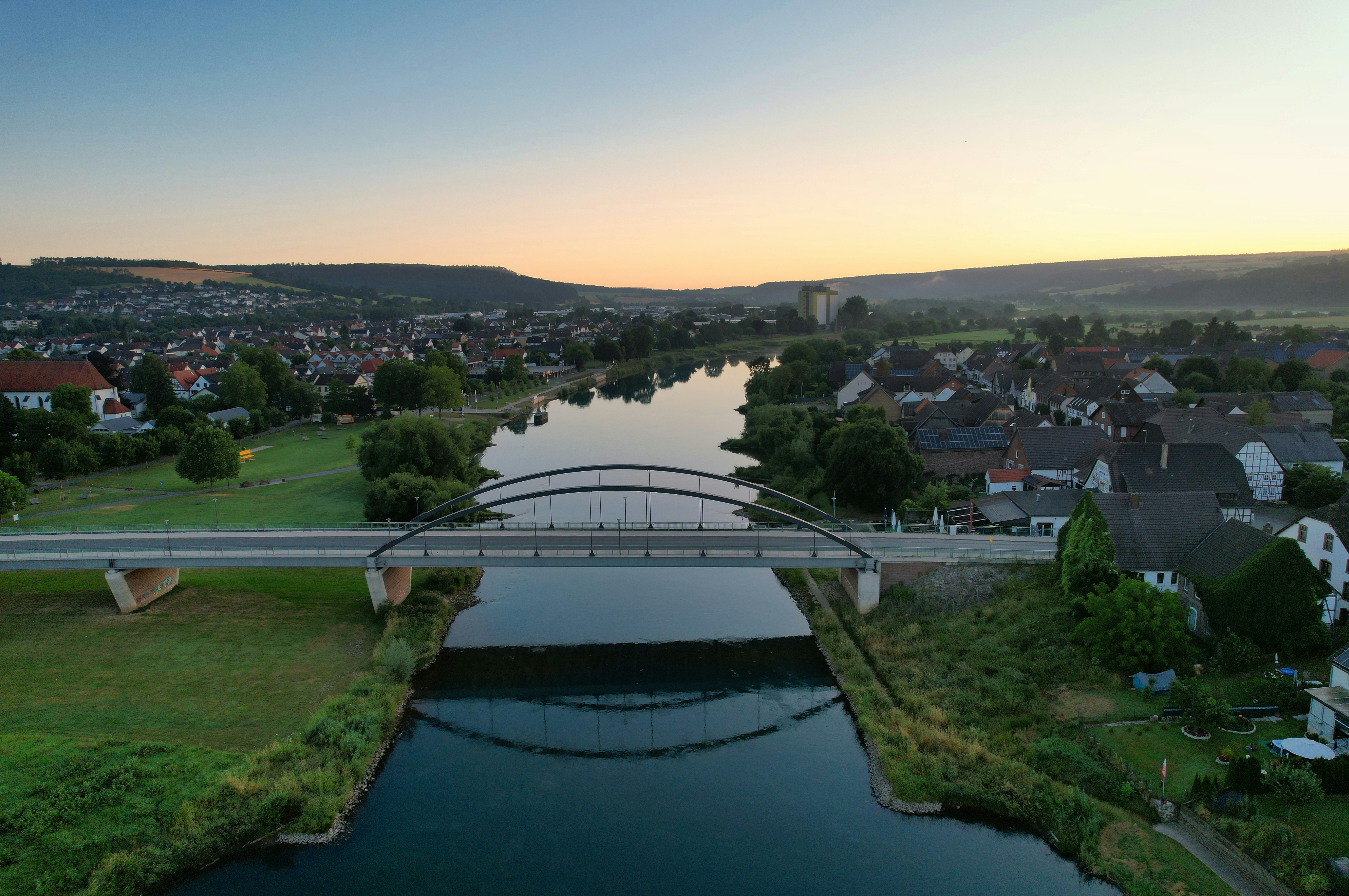 Weserbrücke Beverungen Lauenförde | A bridge spans a river through a town at sunset.