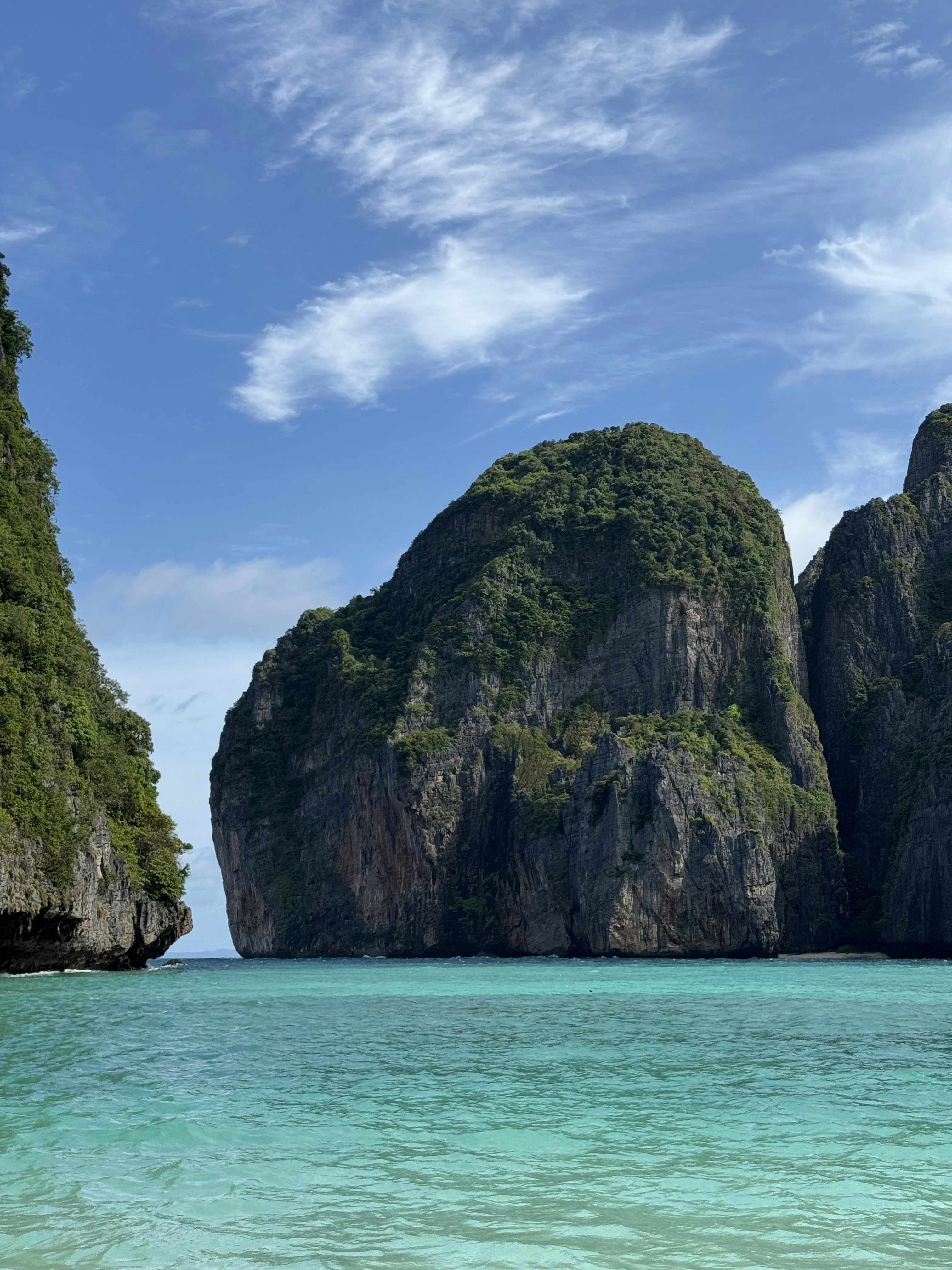 Towering limestone cliffs rise dramatically from the turquoise waters, framed by a clear blue sky with wispy clouds.