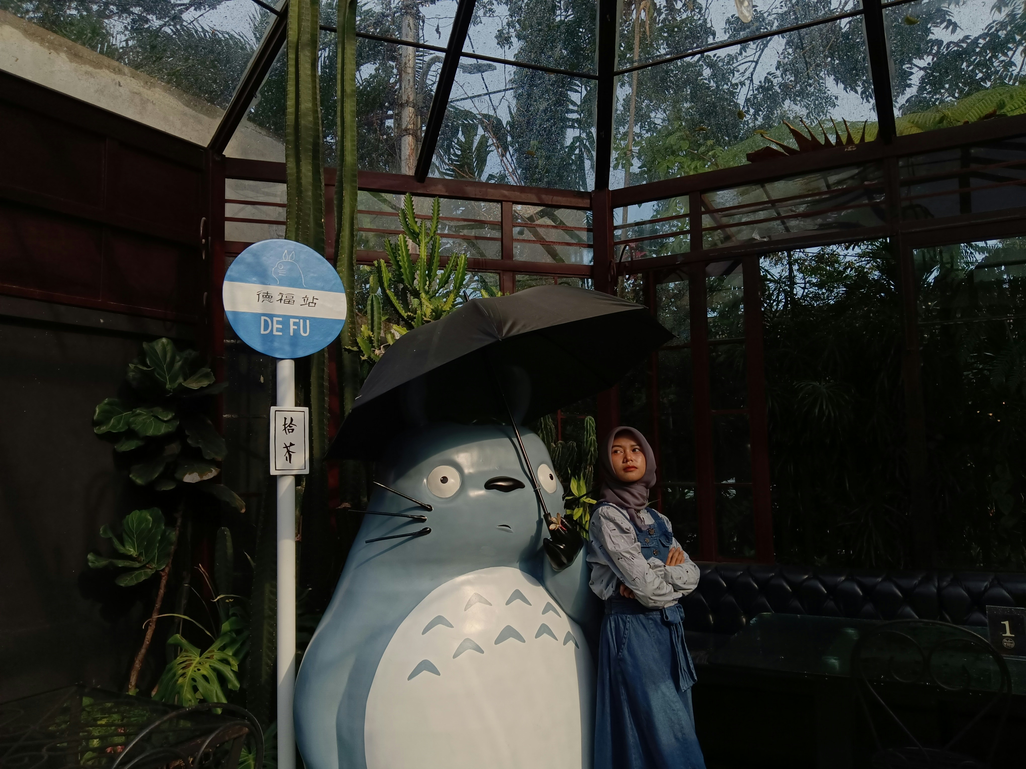 A person and totoro statue pose under umbrellas.