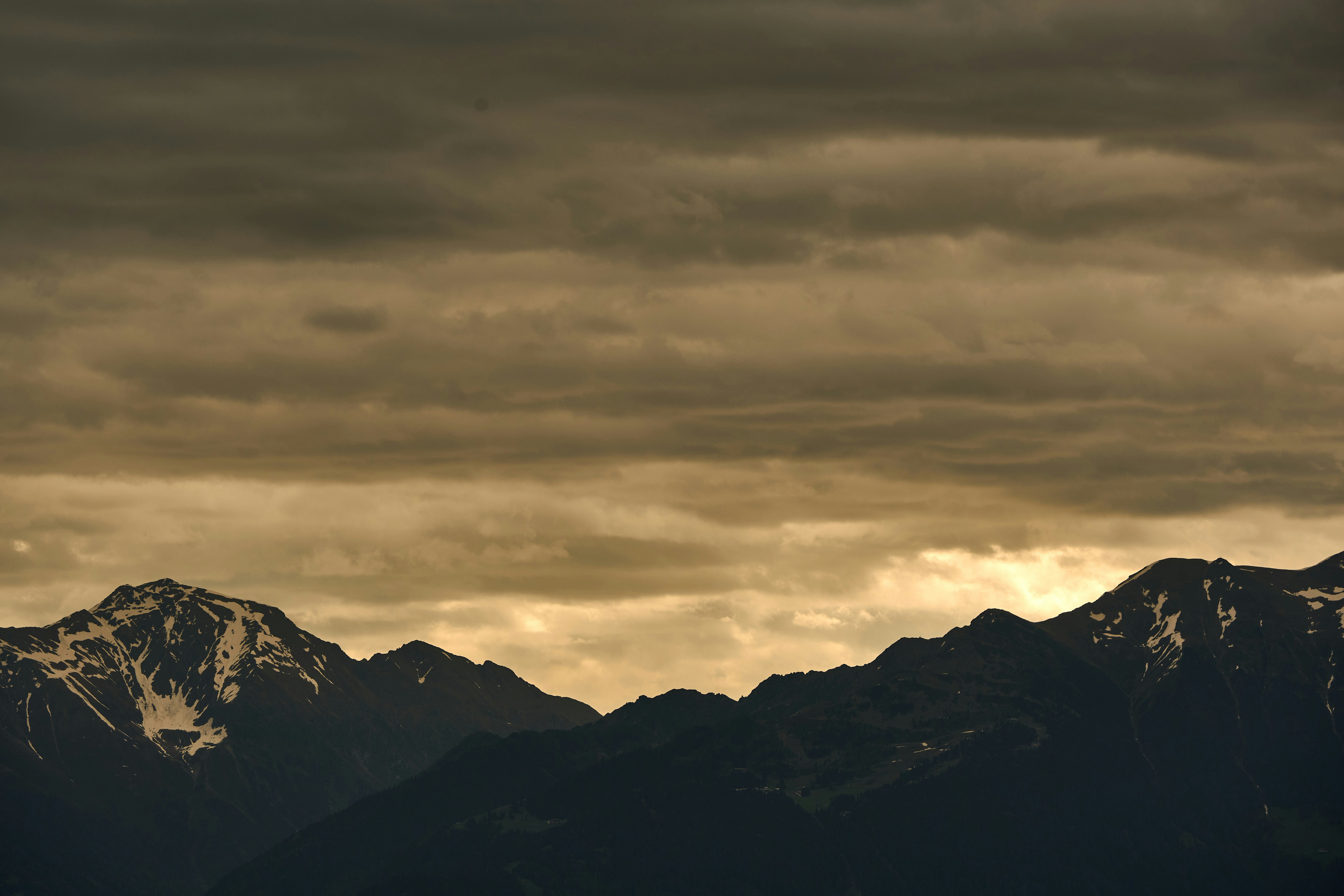 Dramatic mountain range under a moody sky, showcasing snow-capped peaks and a rich, textured atmosphere.