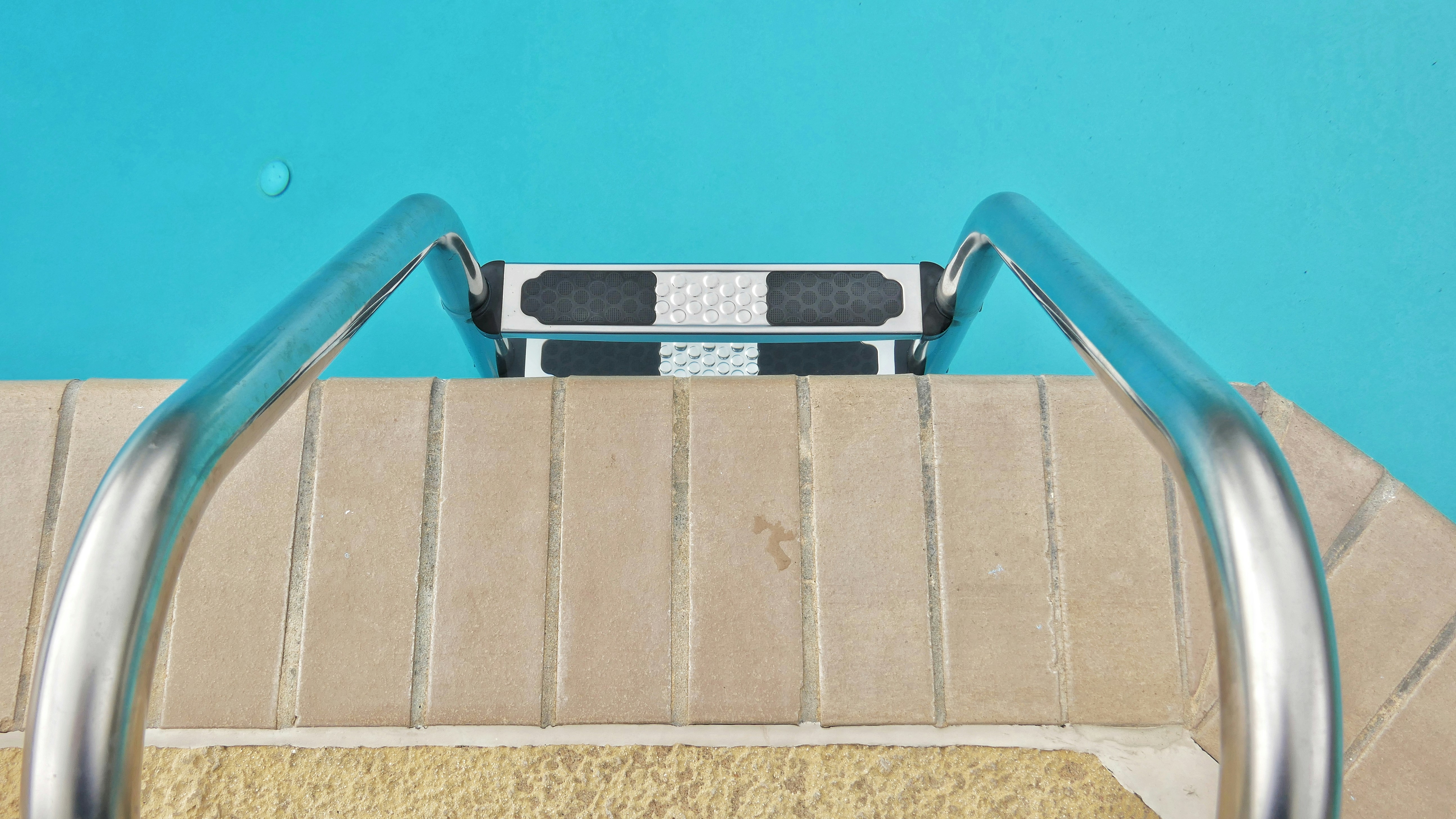 poolside ladder | Pool steps lead into clear, blue water.