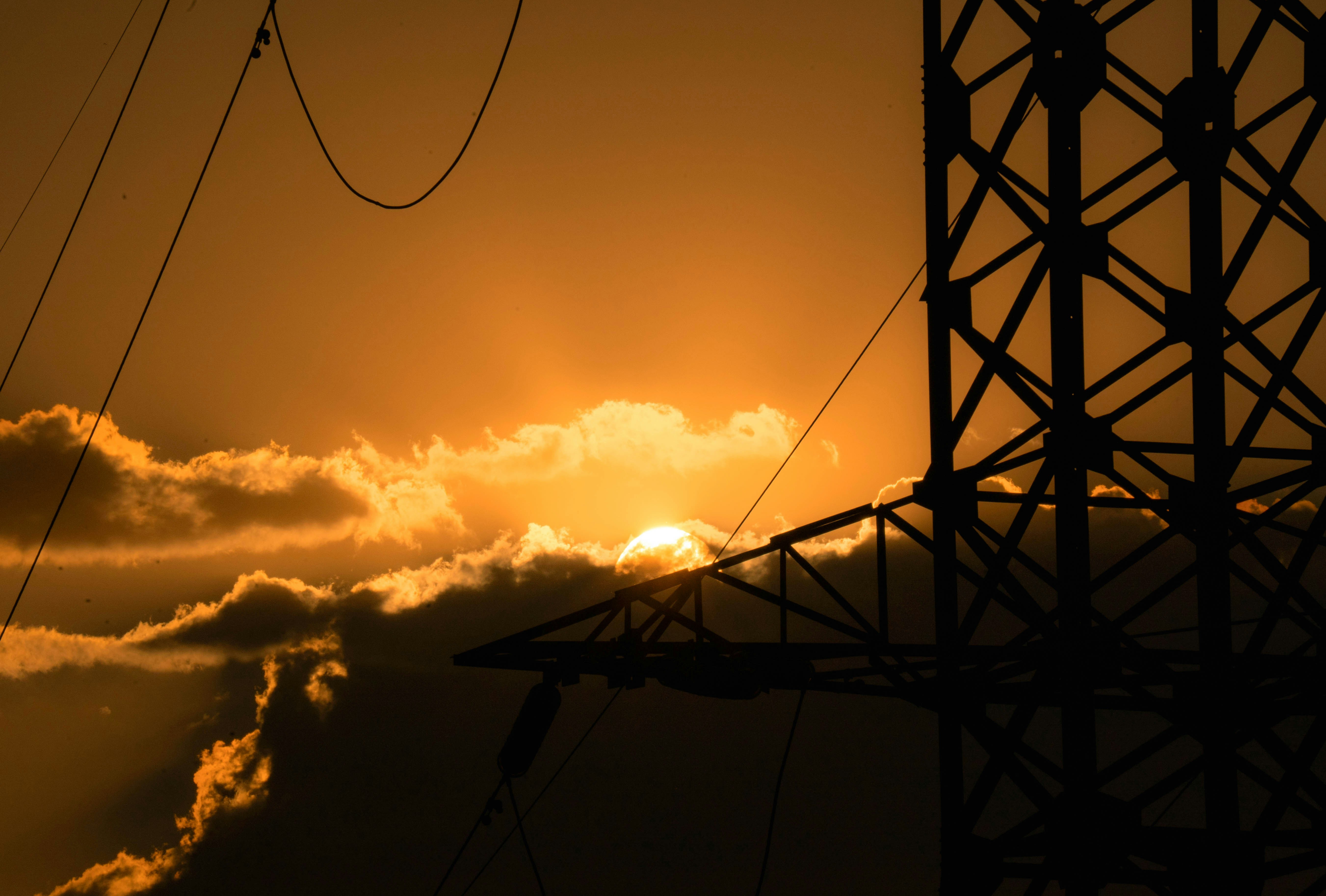 Sunset shines through clouds and a power tower.