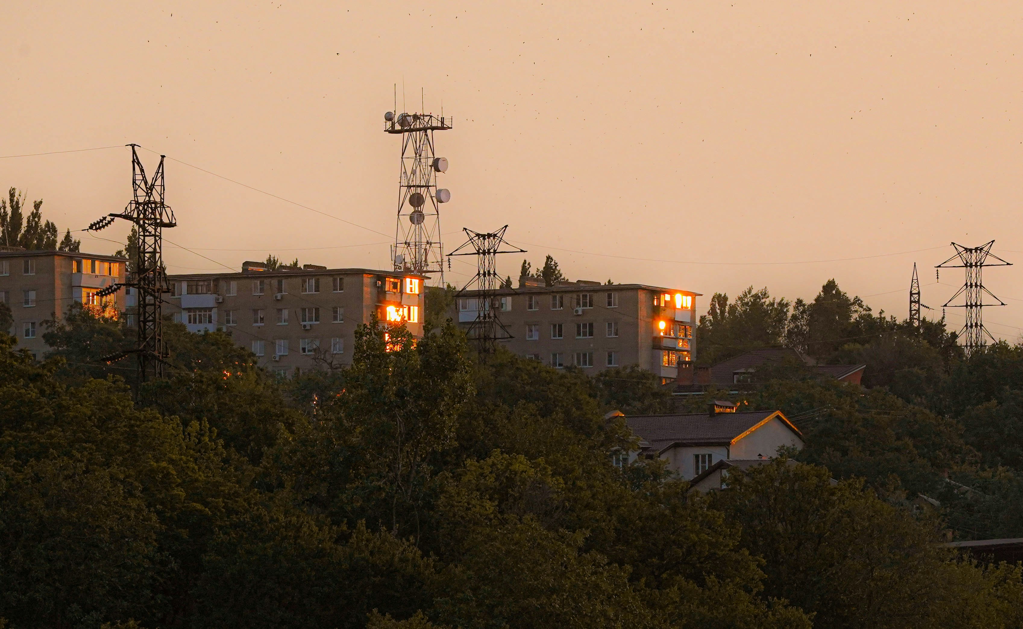 Buildings and power lines are lit by the sunset.