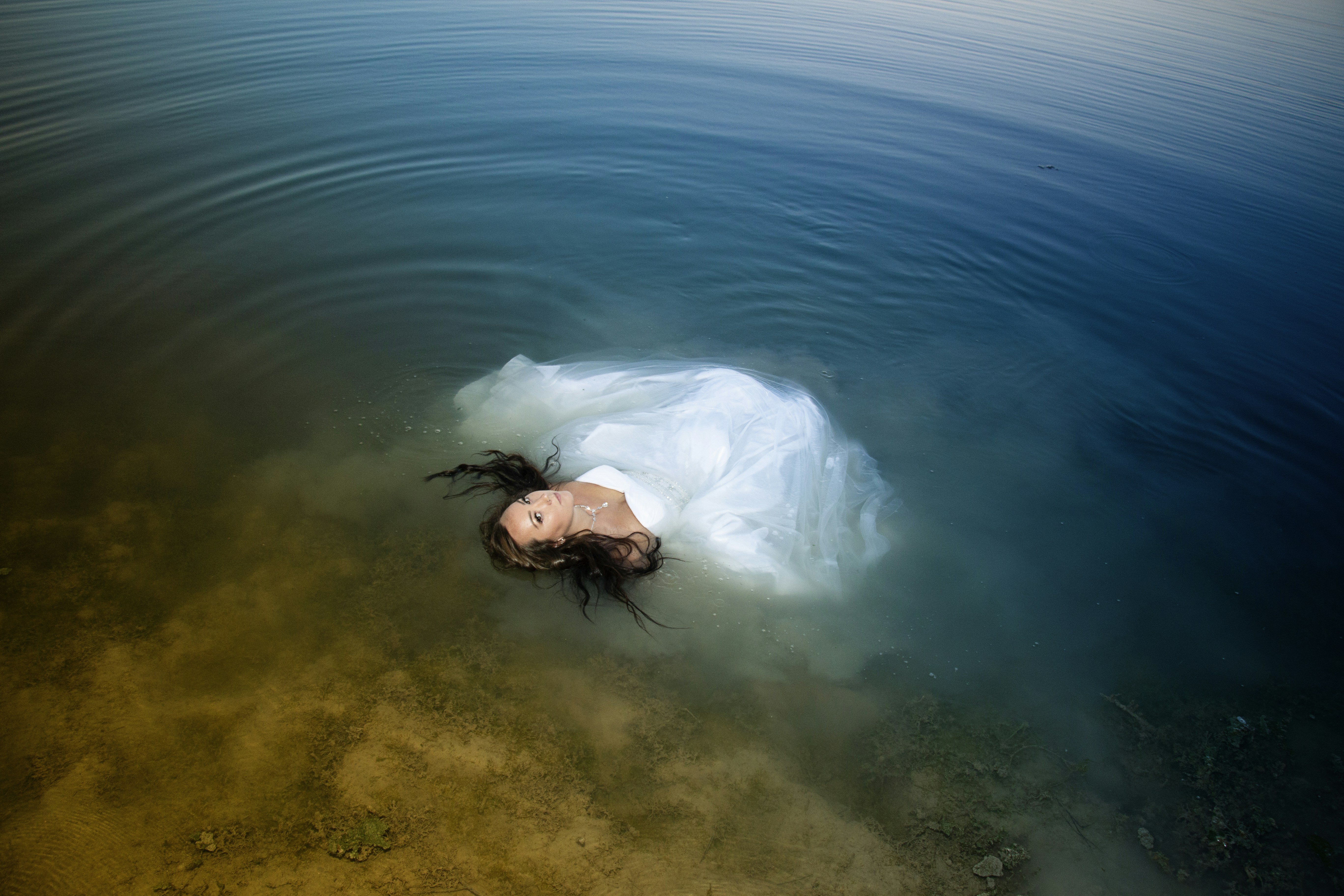 trash the dress, water, wedding dress, trees, woman, dress, daytime, reflection | A person in a white dress is submerged in water.