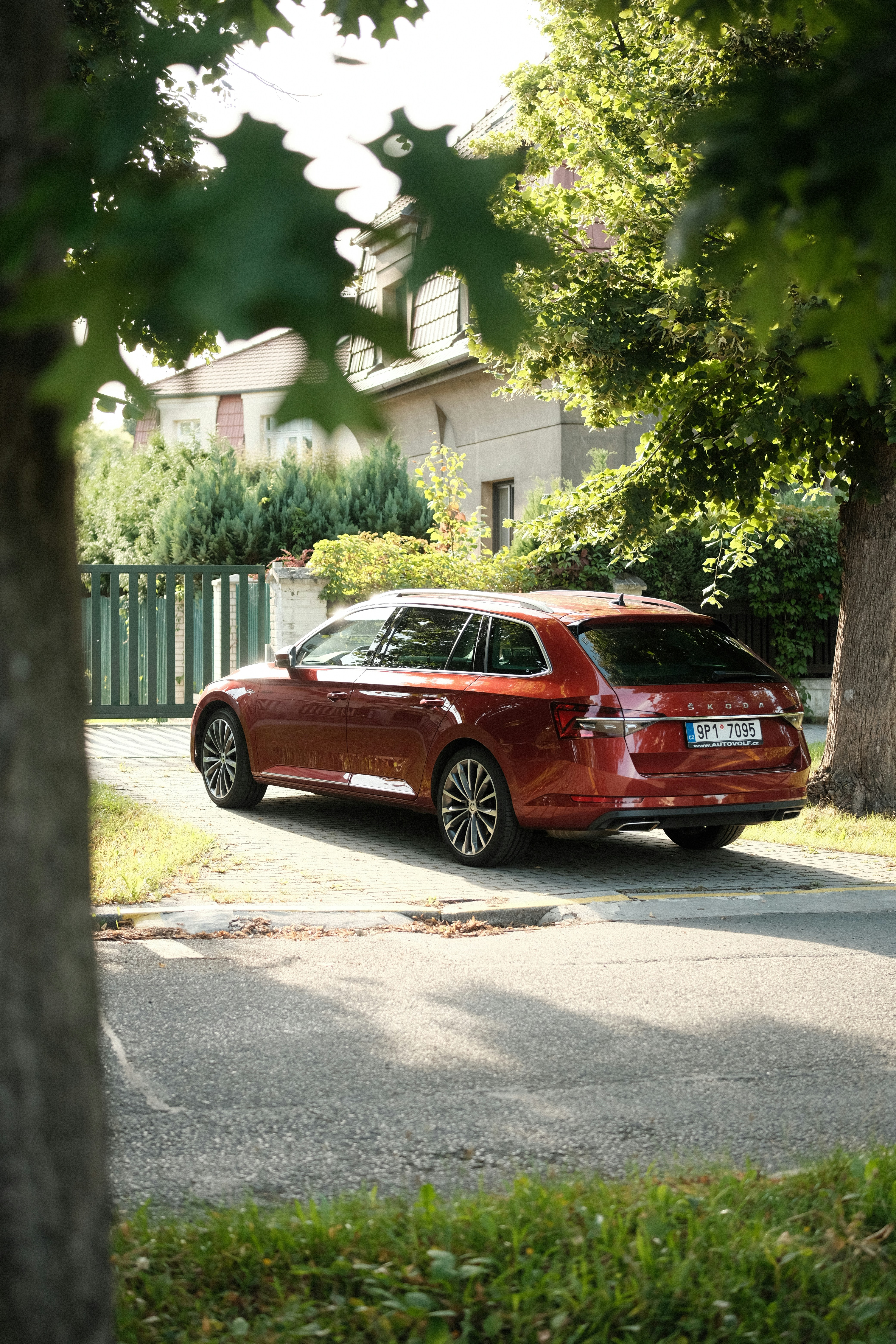 Škoda Octavia. Red car parked beside green fence in residential area | A red wagon car parks on a street.