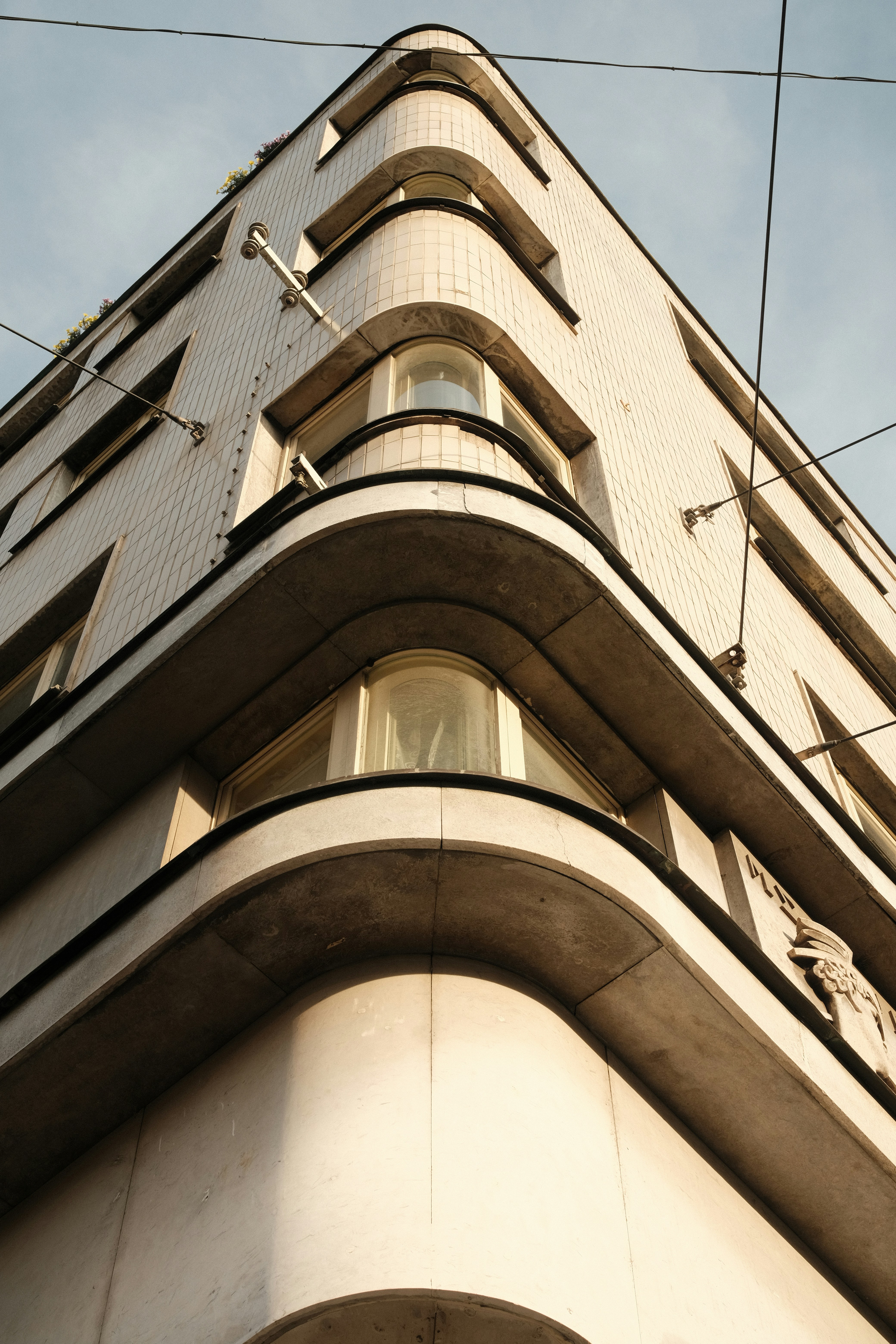 The image shows the exterior of a modern building with curved edges and large windows. The perspective is from the ground looking up, capturing the details and angles of the structure. | Unique architecture showcasing a building's angular design.