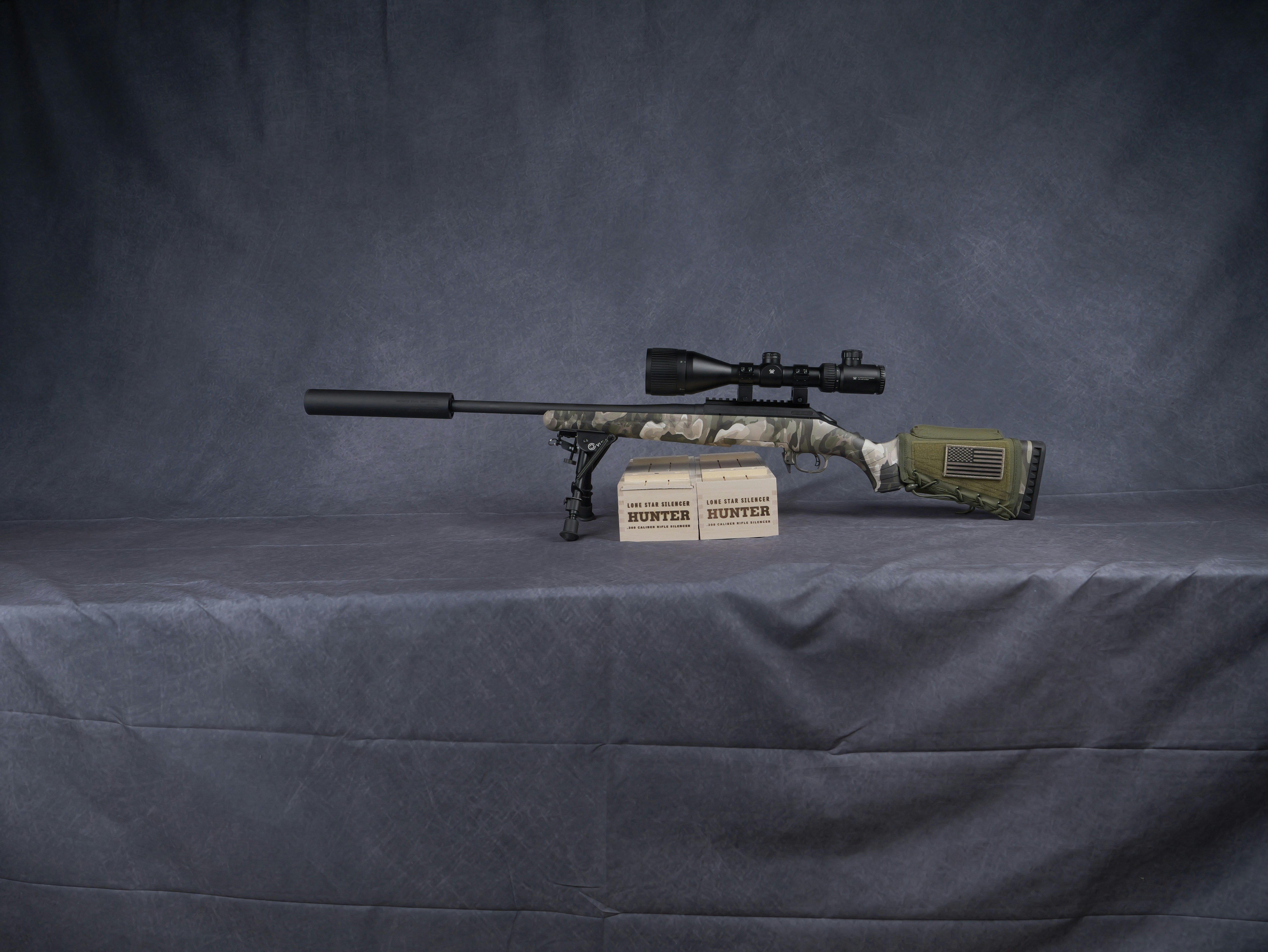 Camouflaged hunting rifle with Lone Star Silencer, hunter edition silencer. | A camouflaged rifle with scope and silencer.