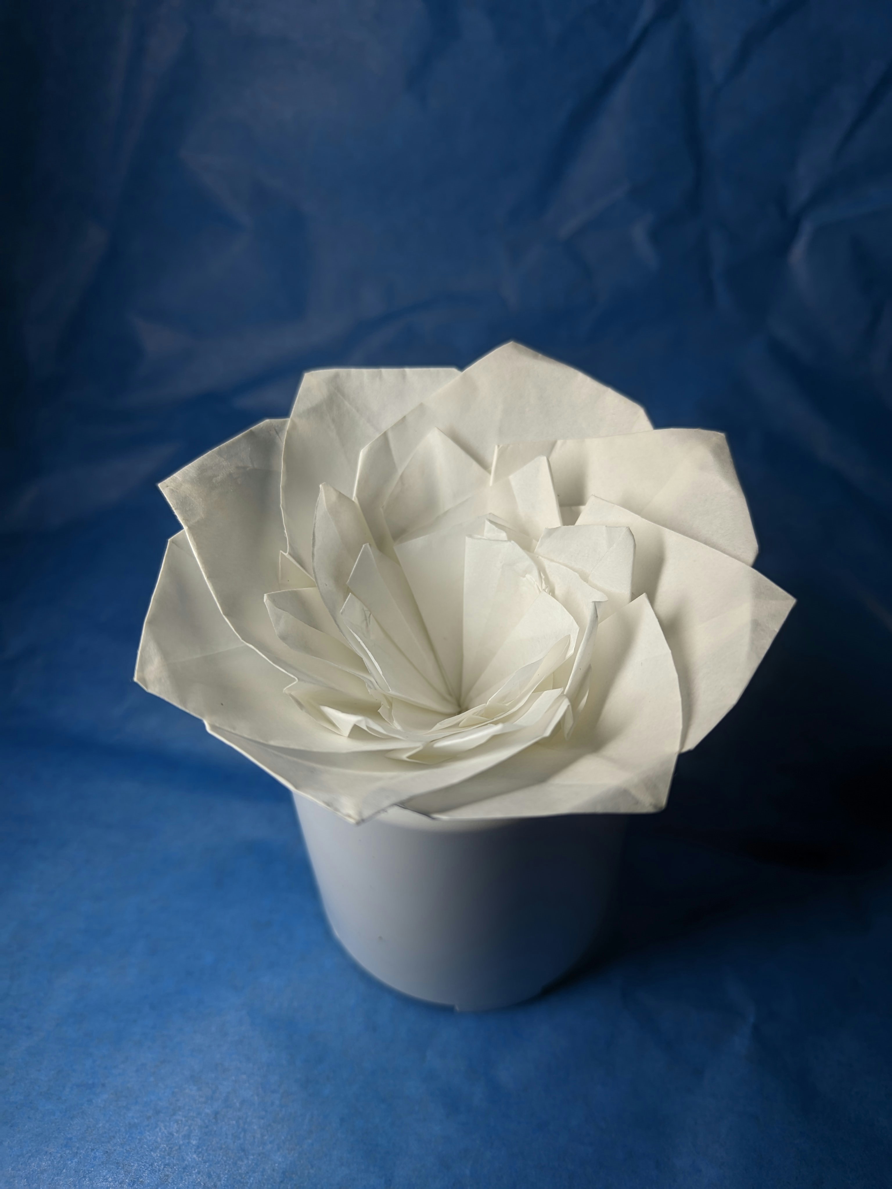 Origami flower decorates a white vase.