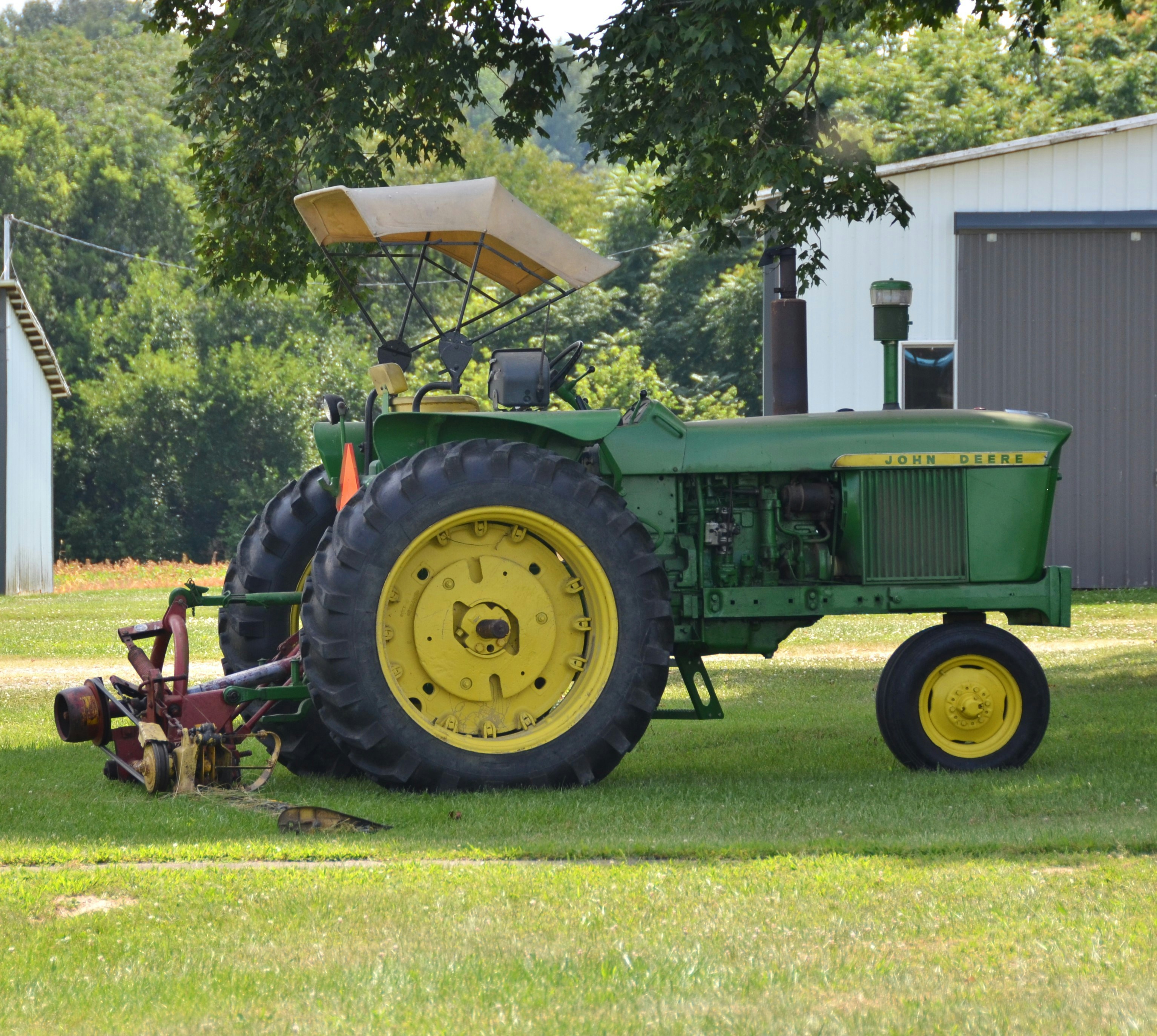 Vintage John Deere tractor with sun canopy and sickle bar mower | A green john deere tractor sits on green grass.