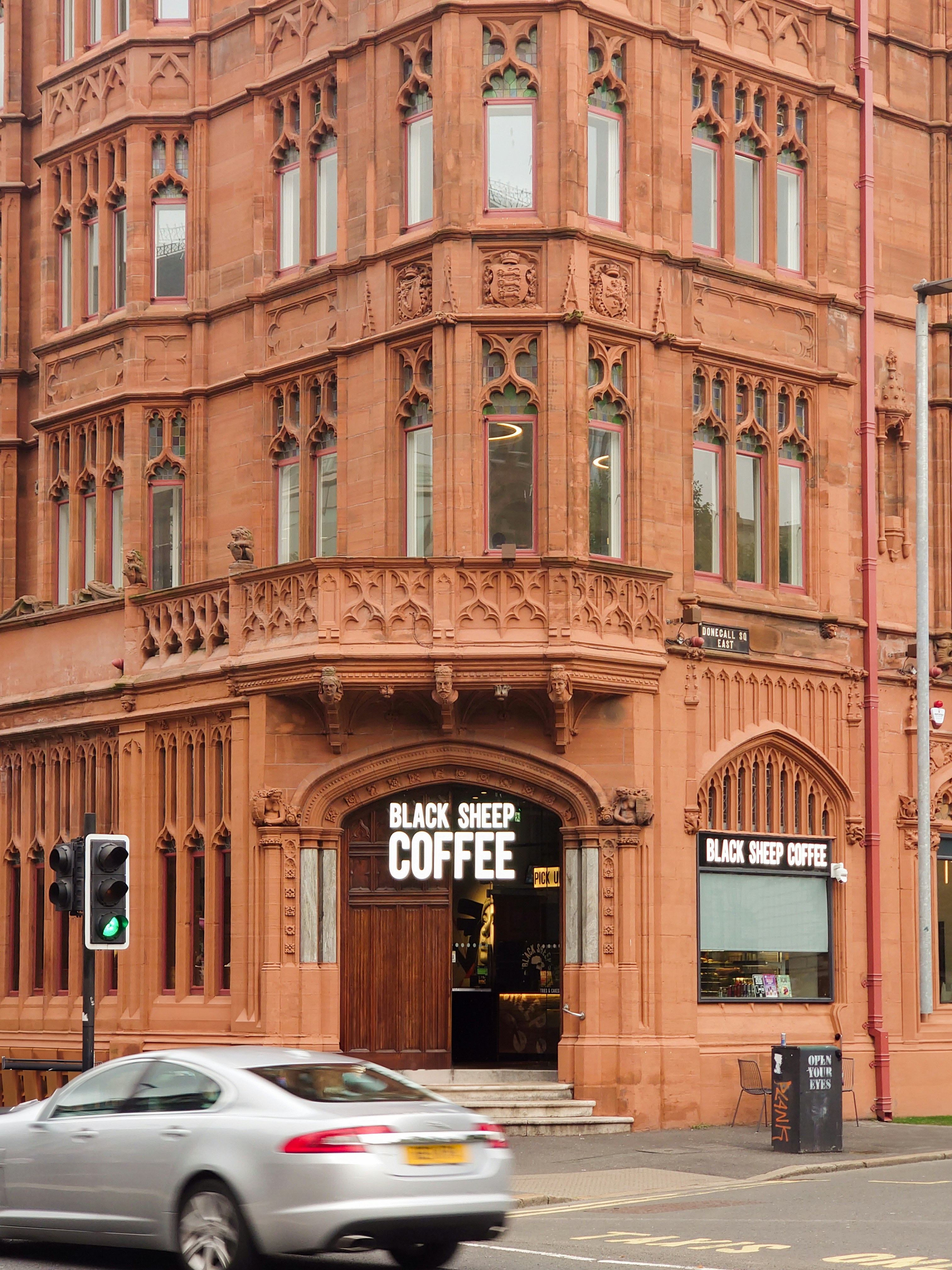 Victorian-style building housing Black Sheep Coffee, featuring intricate architectural details and large windows. A car passes by in the foreground.