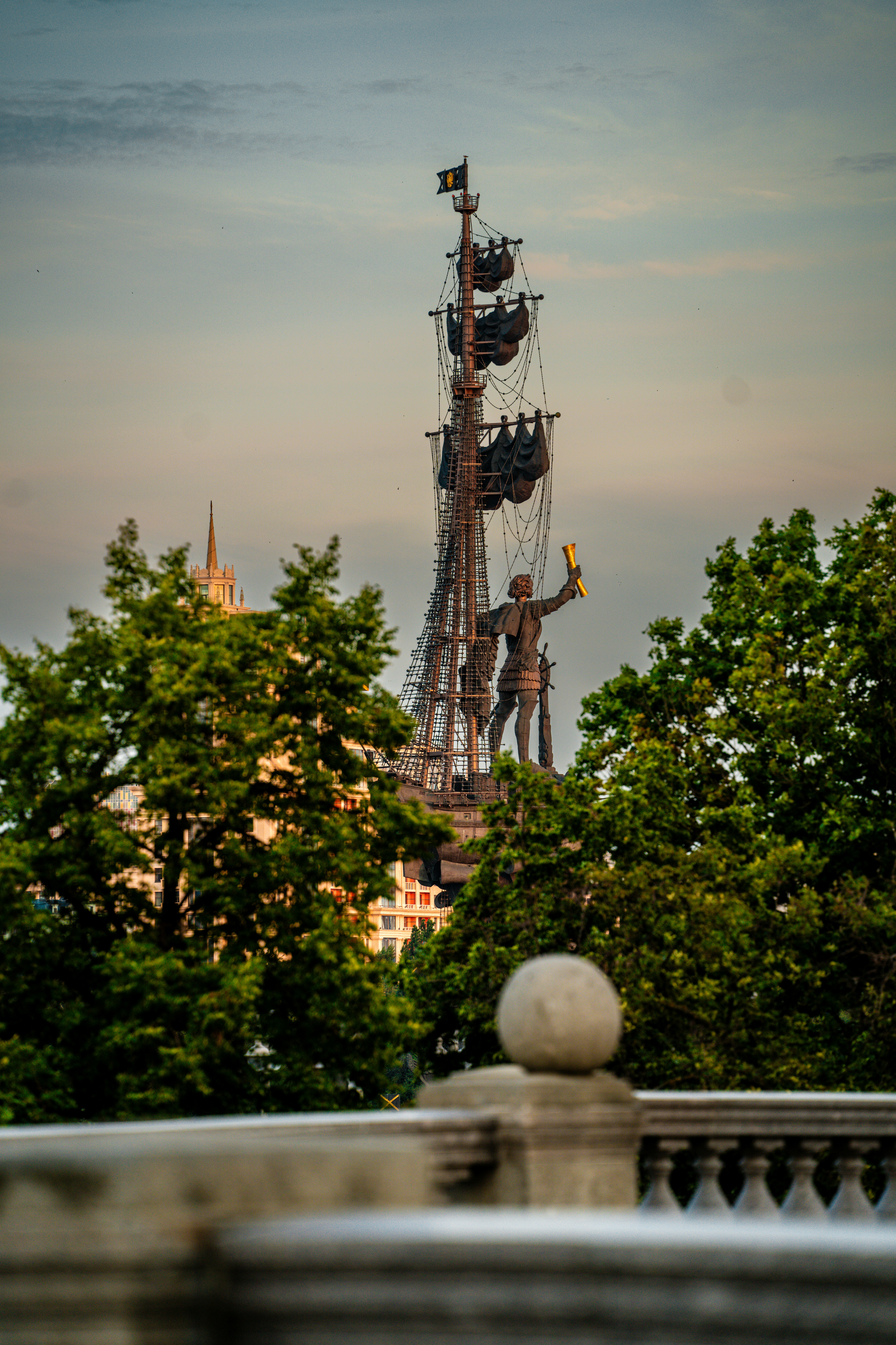 Ship silhouette atop a monument: a cityscape framed by trees at golden hour