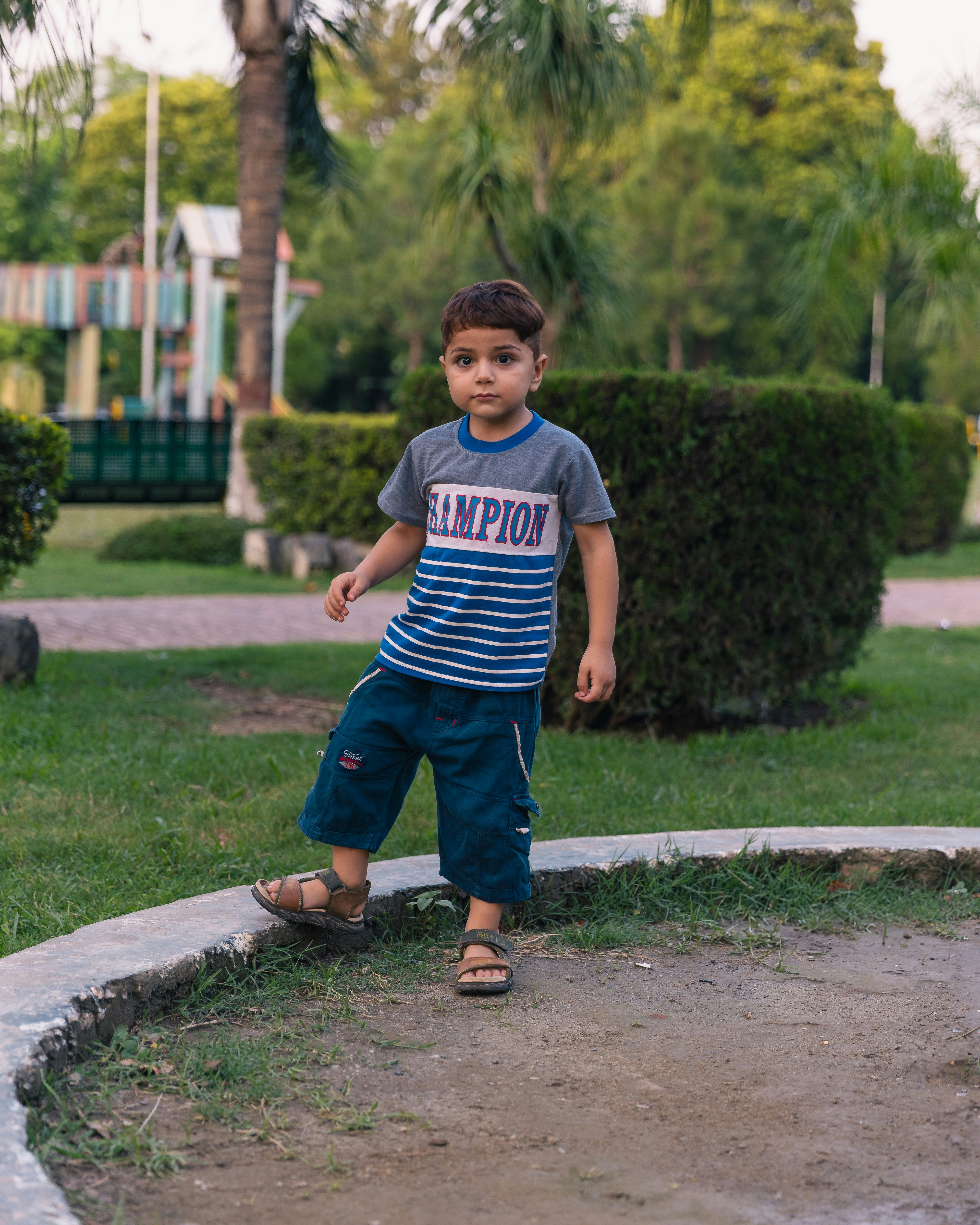 Young boy standing in a park with trees.