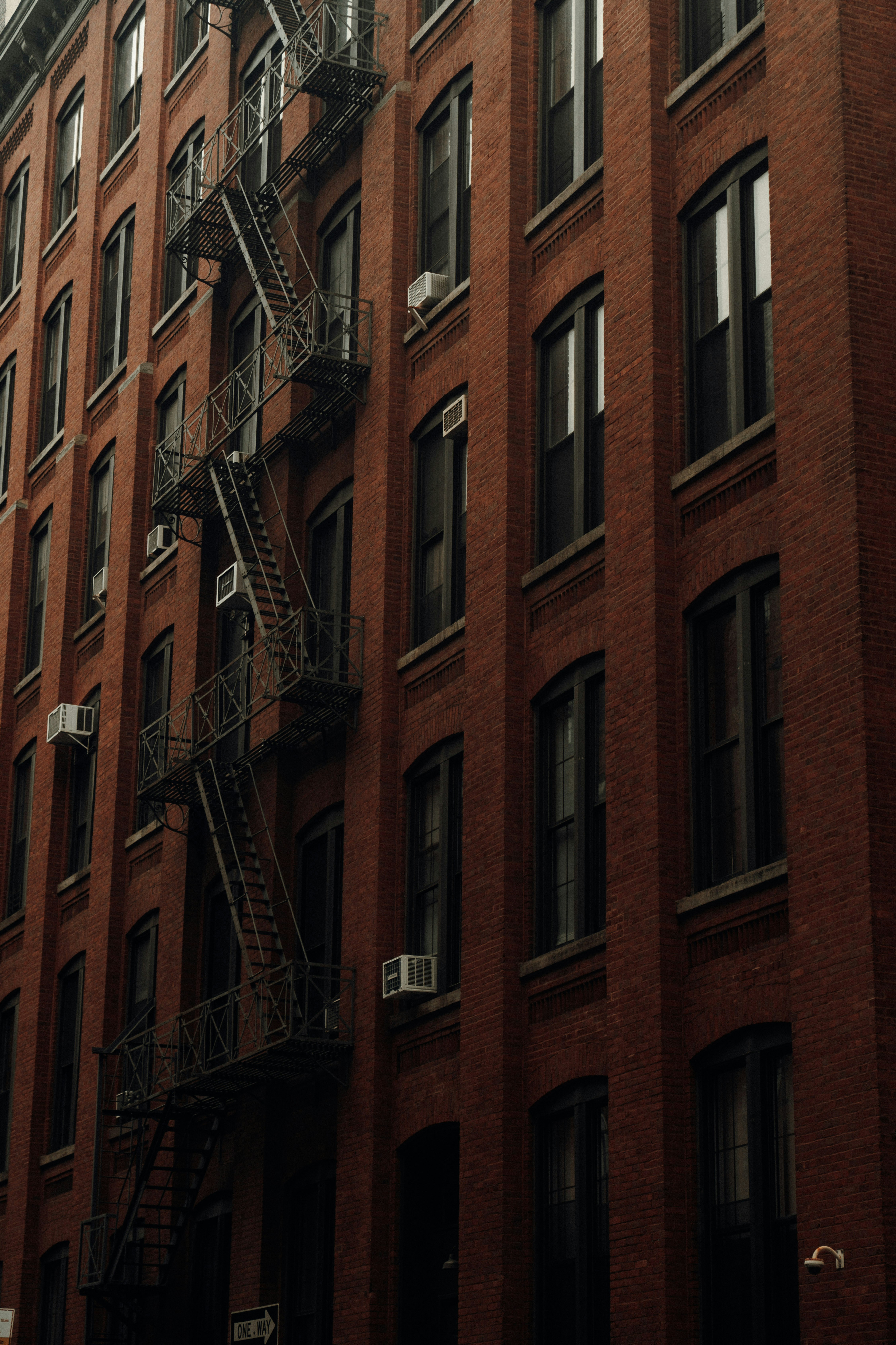 A detailed view of a brick building facade featuring a metallic fire escape and air conditioning units, showcasing urban architecture's functional design.