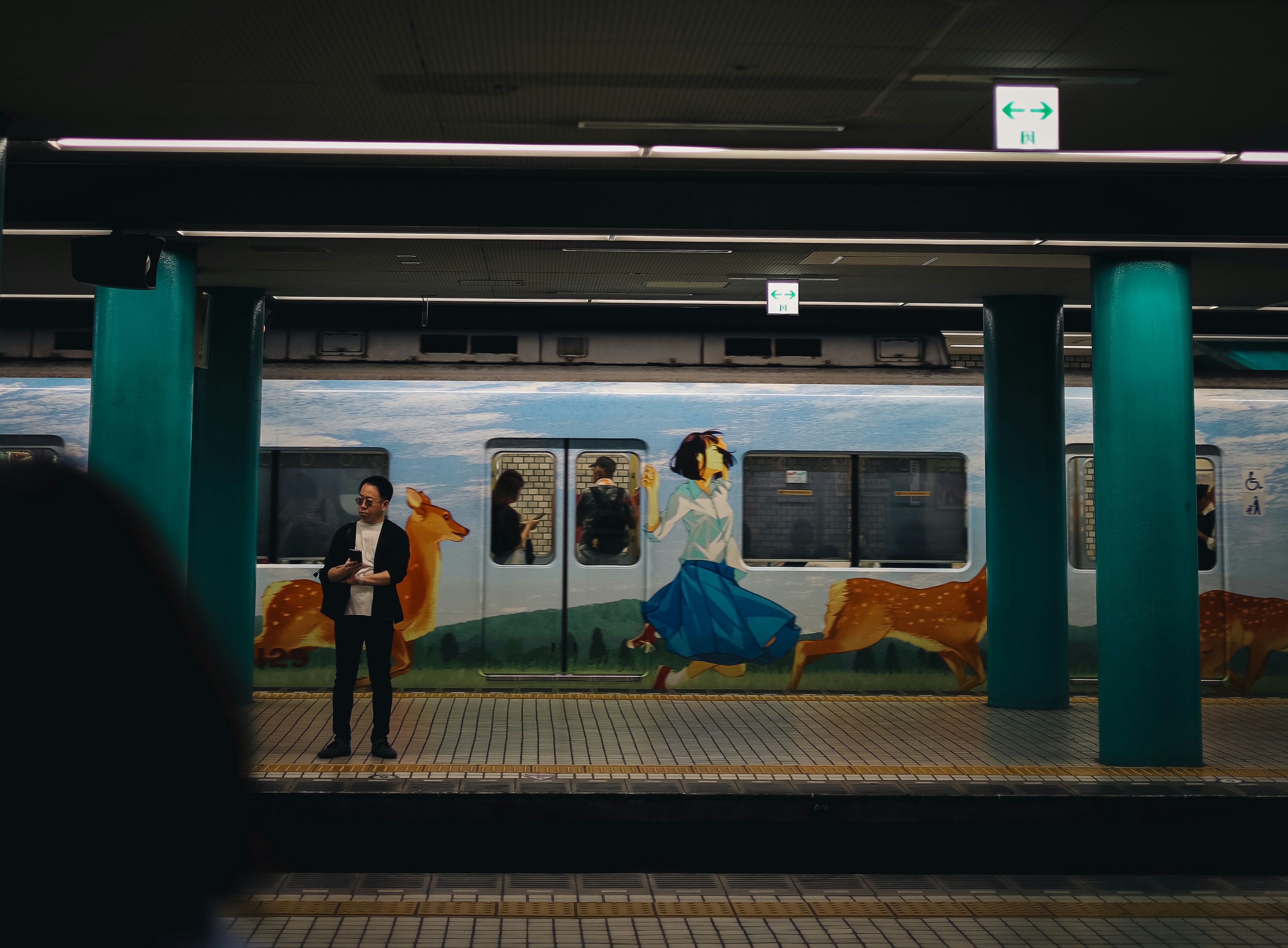 A subway platform scene featuring a mural of a woman in a blue dress interacting with deer, while a passenger waits nearby, creating a contrast between urban life and nature.