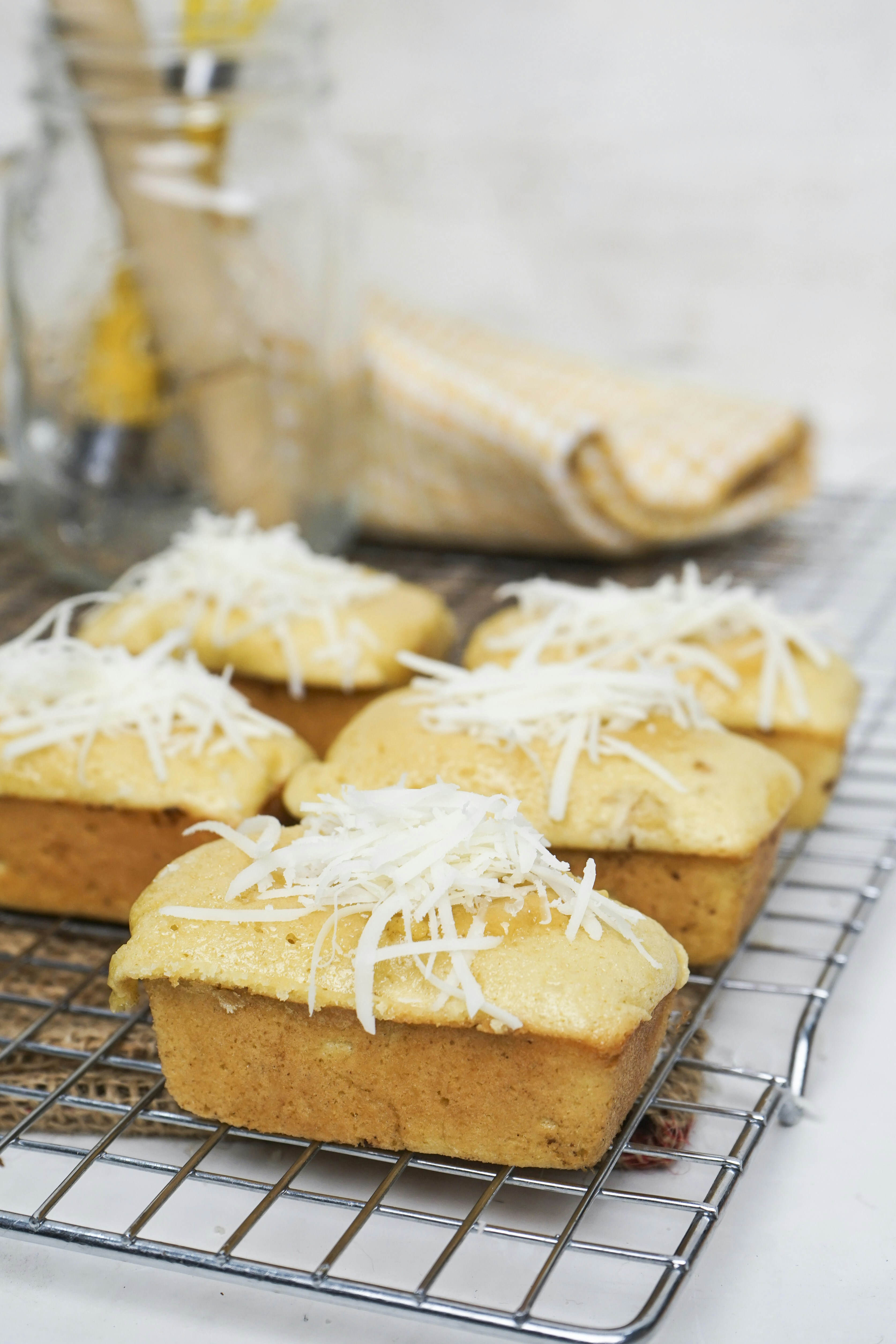 Freshly baked mini loaves topped with shredded cheese, resting on a cooling rack. A cozy kitchen scene with soft, natural lighting.