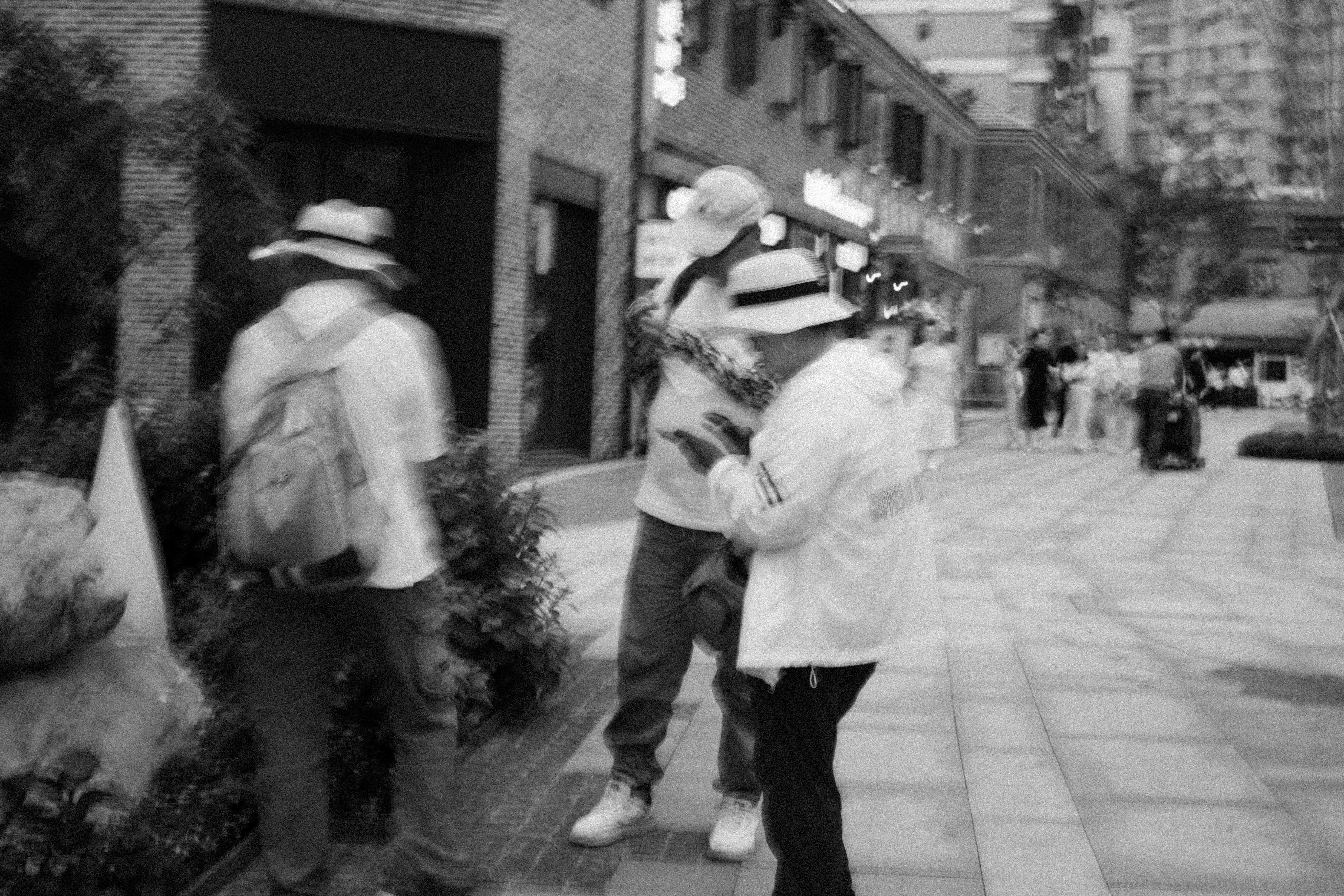 Three individuals in white attire engage in conversation on a bustling urban street, surrounded by brick architecture and greenery.