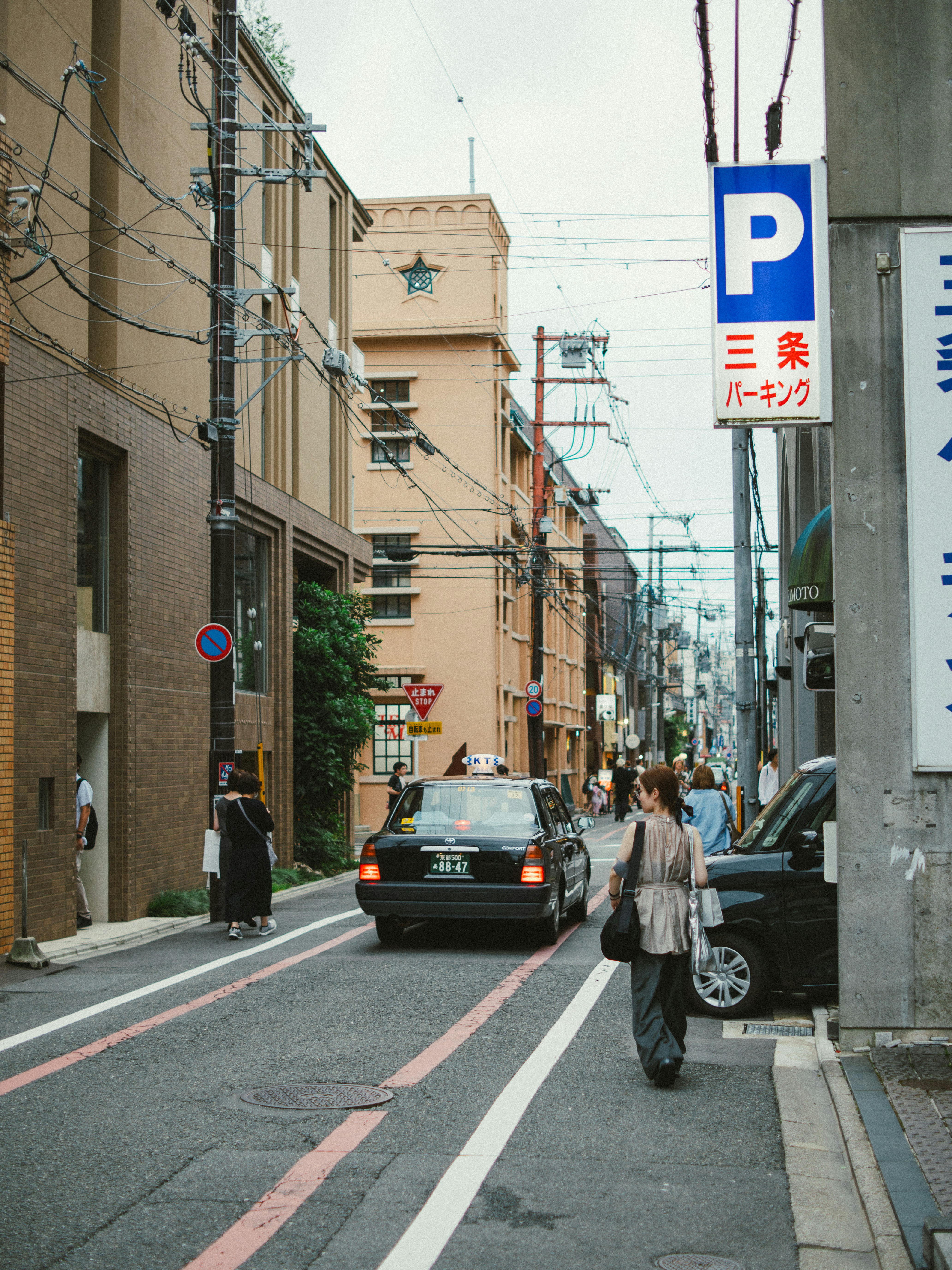 A japanese street scene with a taxi and pedestrians.